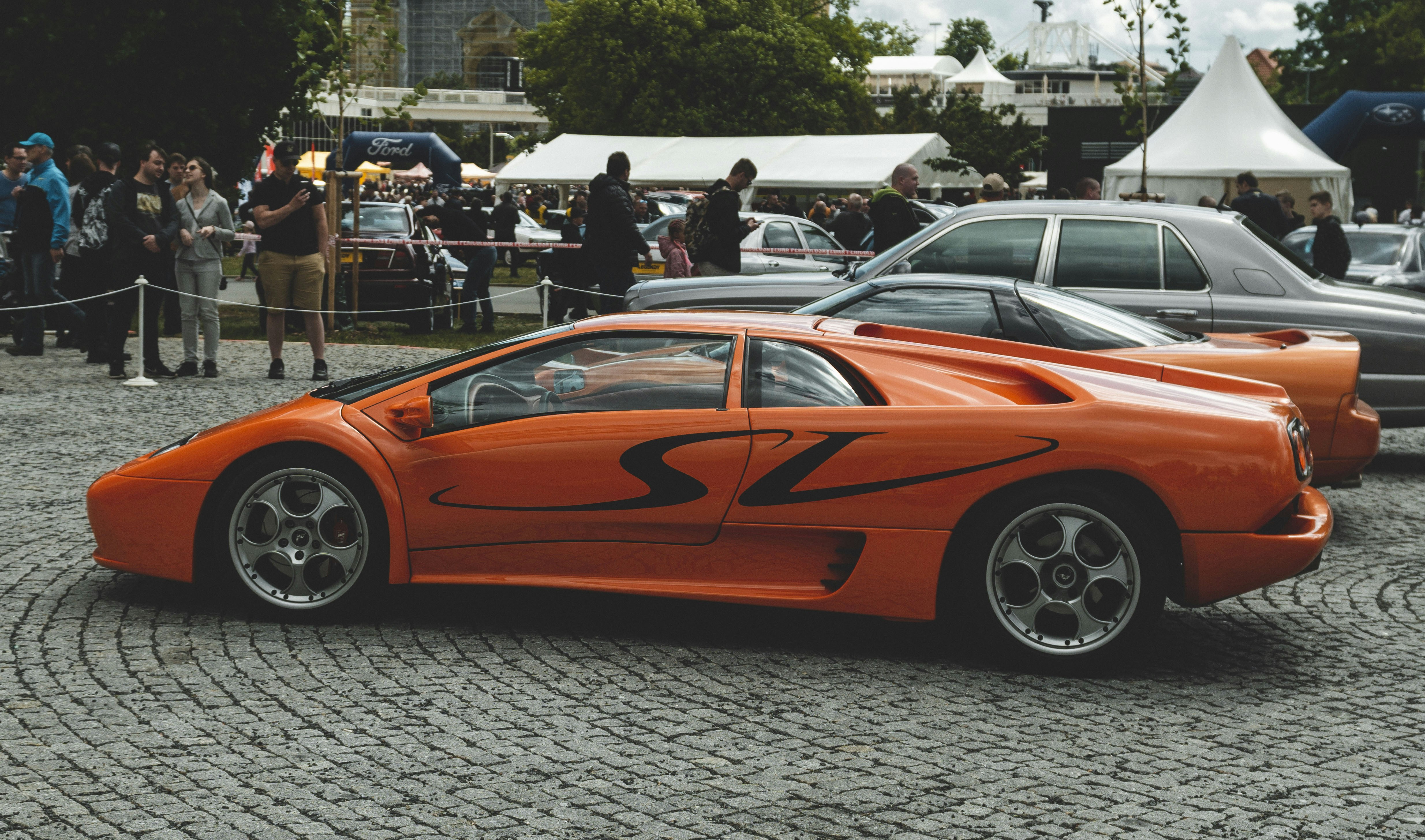 Scarlet Slipstream on Cobblestones: An Orange Hypercar Commands a City Car Show