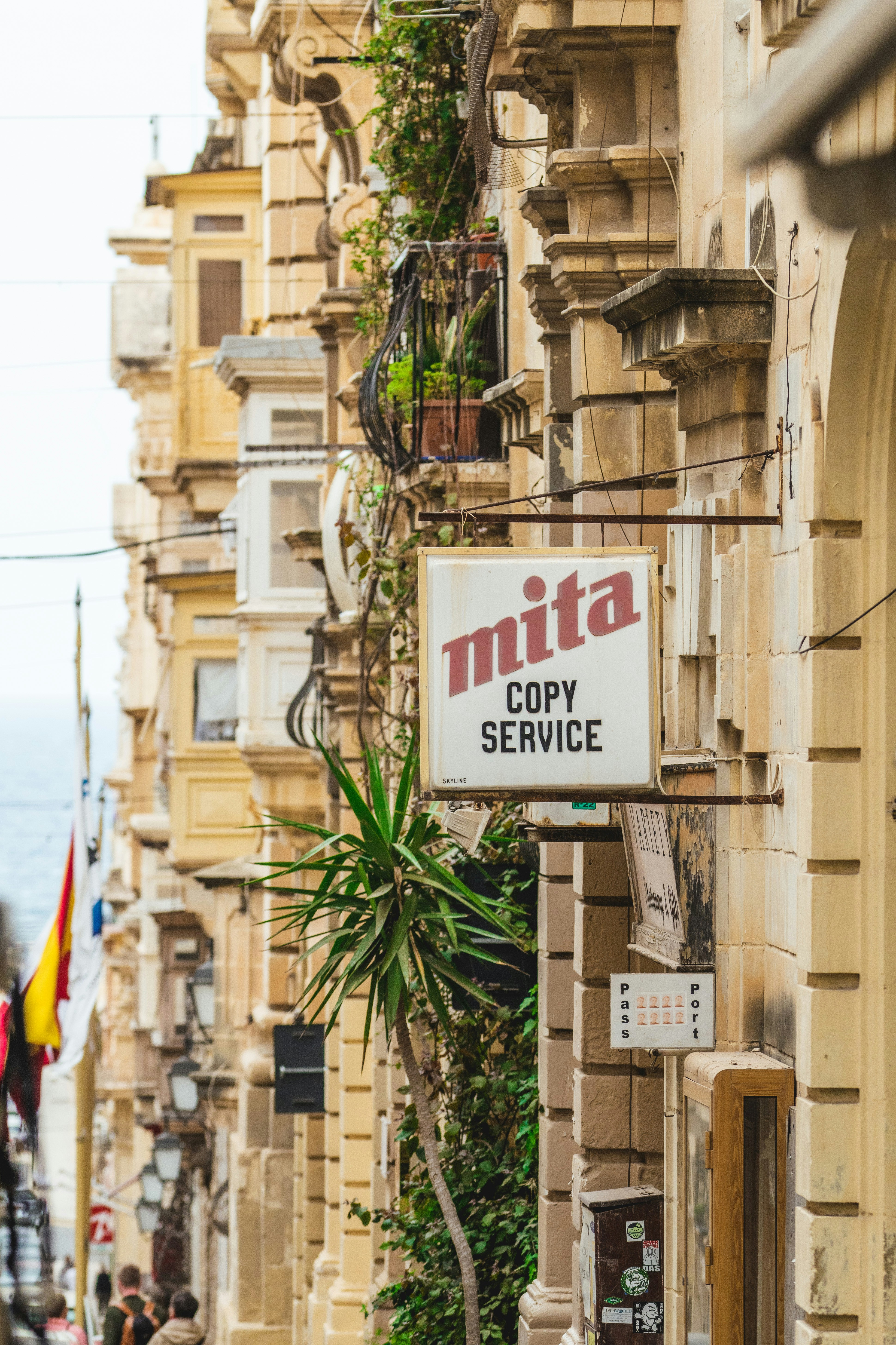 Sign for 'mita COPY SERVICE' amidst charming architecture and greenery in a bustling urban setting.