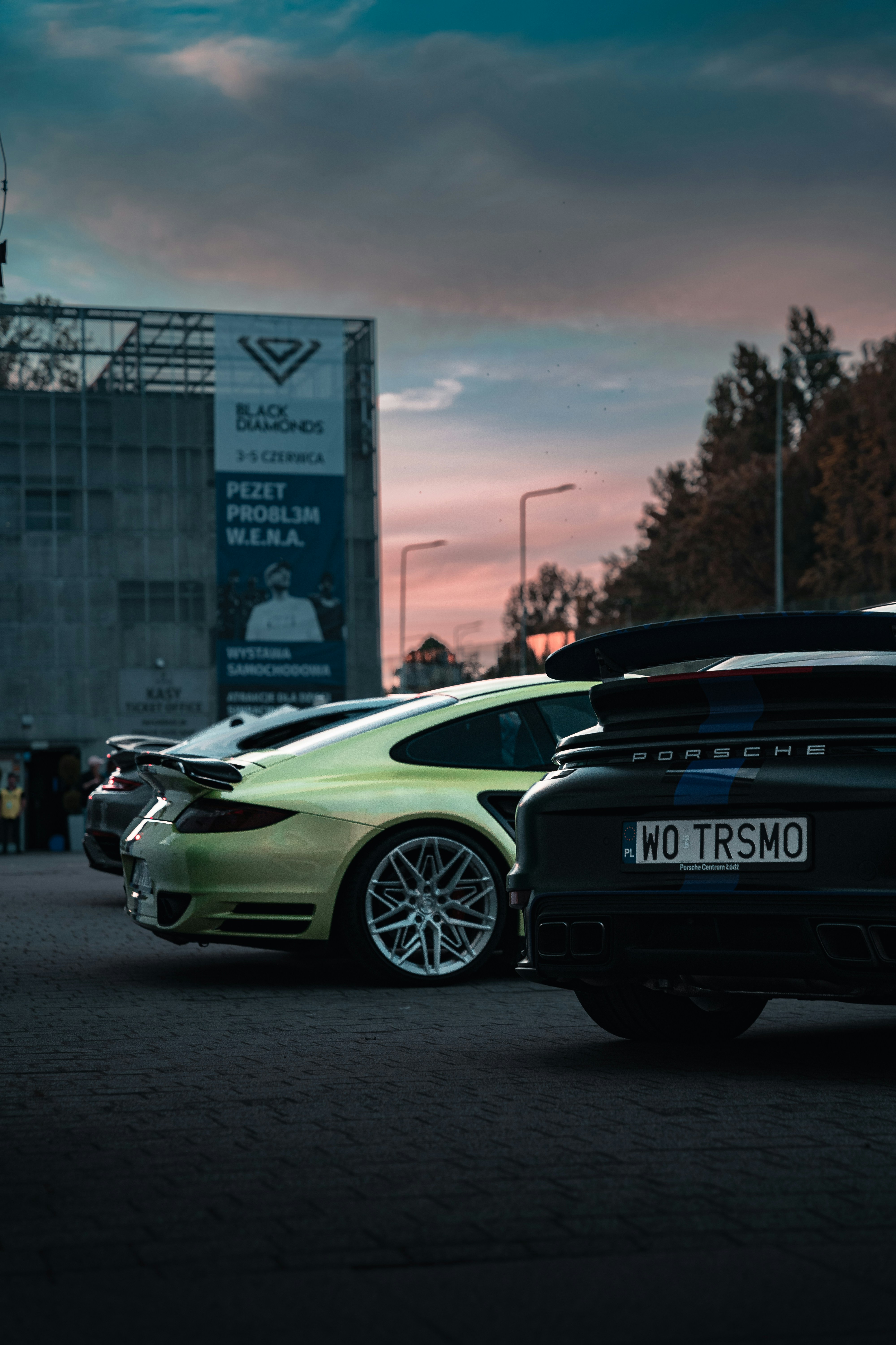 Two Porsche sports cars parked against a twilight backdrop, showcasing sleek lines and vibrant colors. The scene captures the essence of automotive elegance.