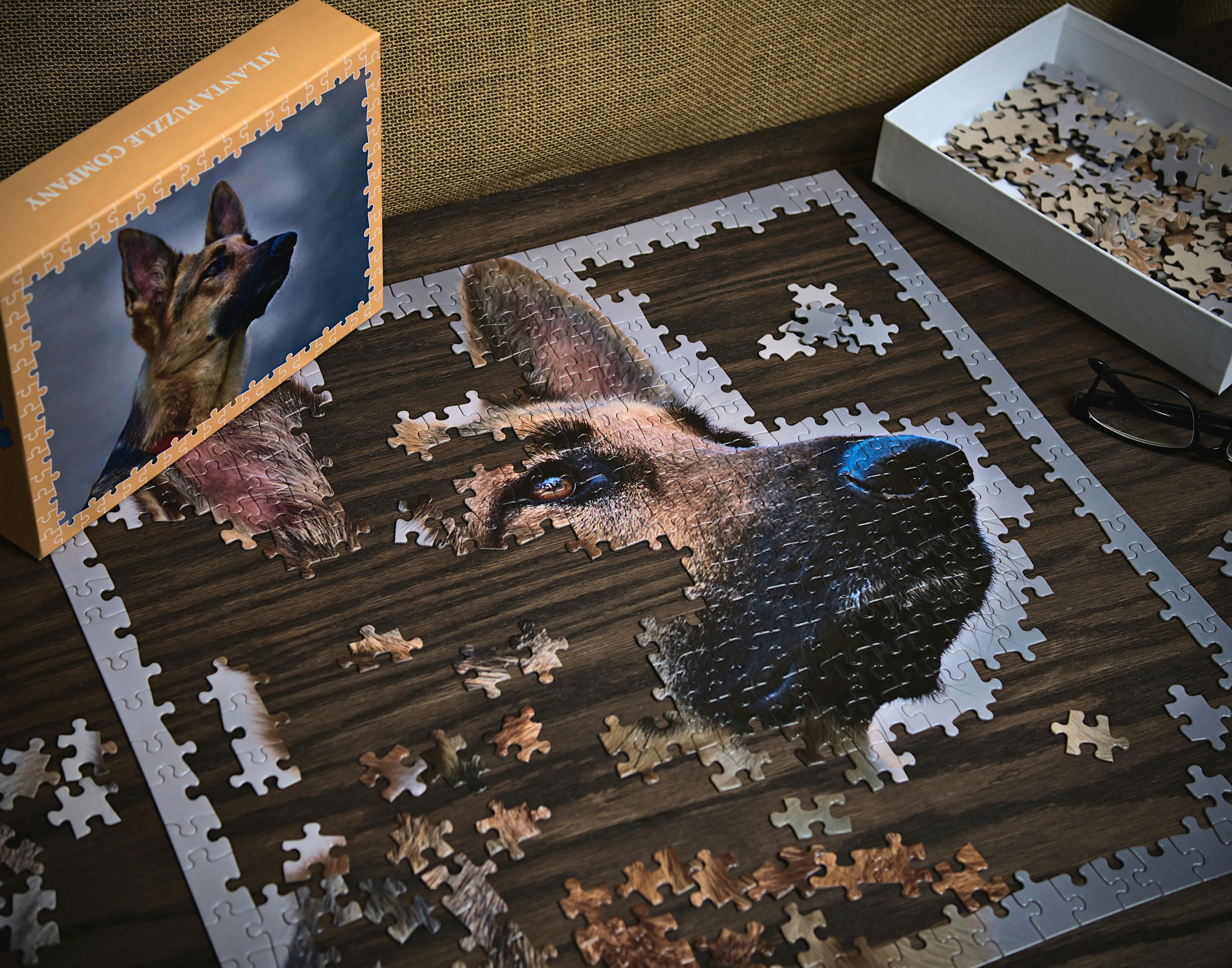 Partially completed cat puzzle on a wooden table beside a box and scattered pieces.