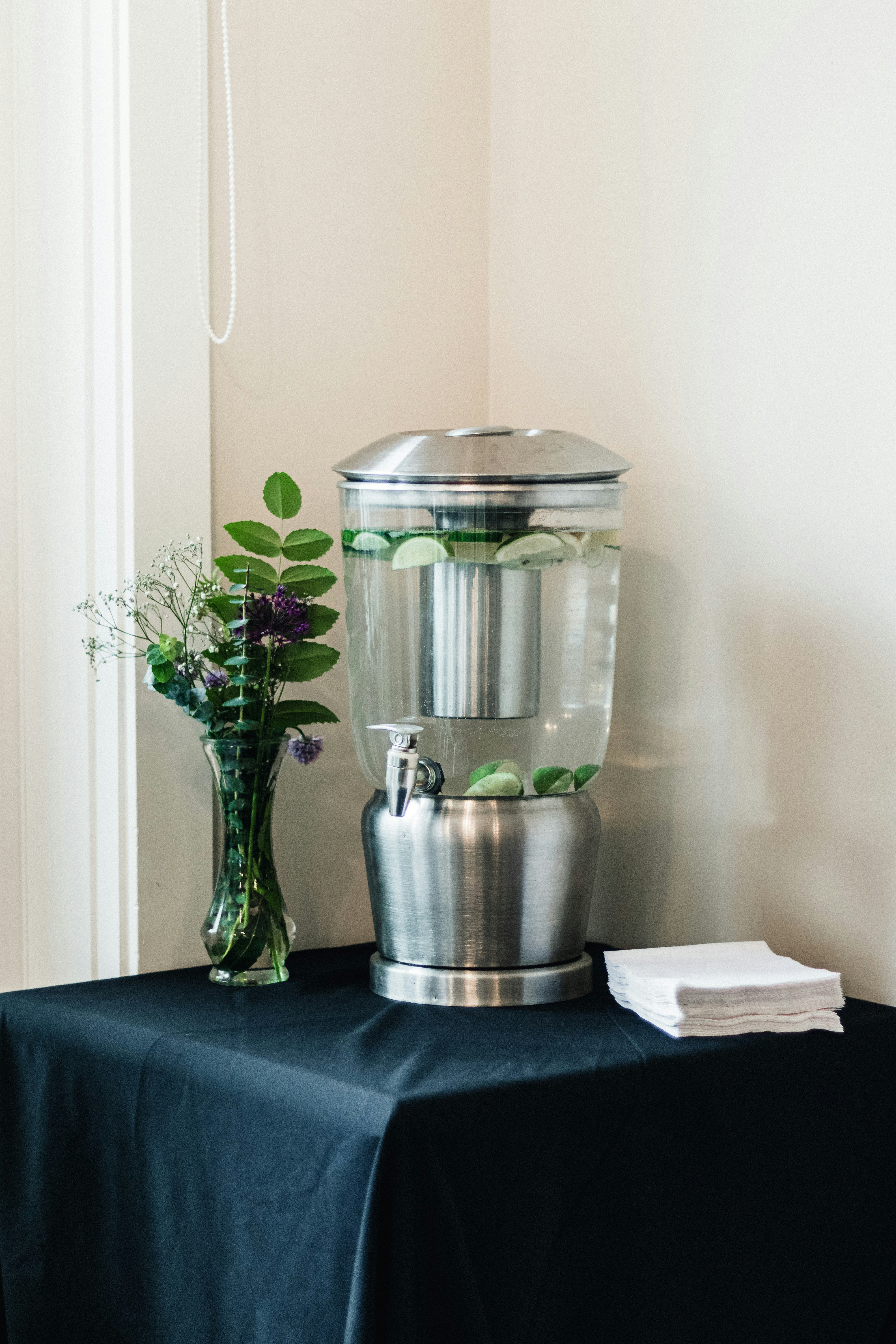 a silver blender sitting on top of a table next to a vase of flowers