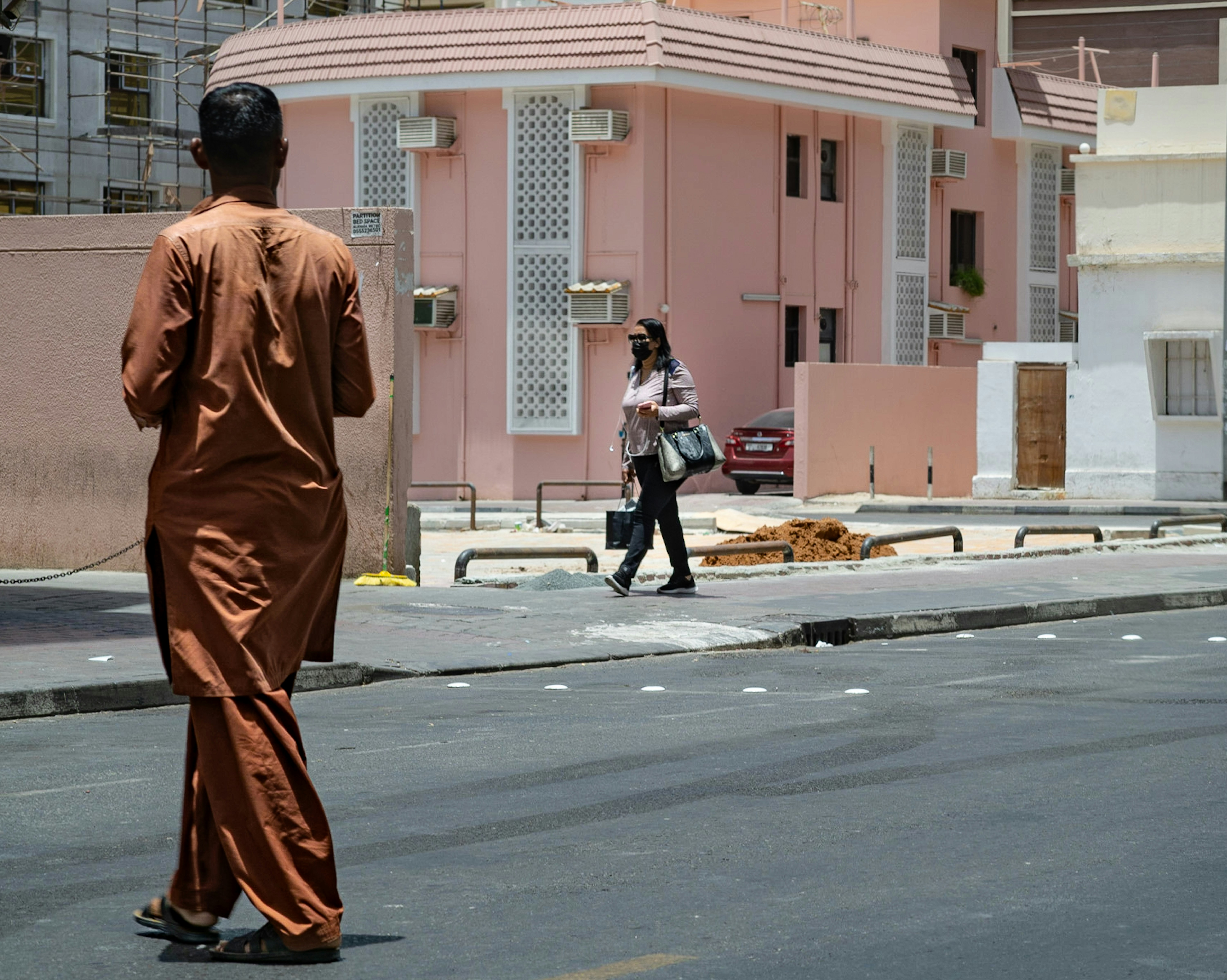 Man in traditional attire walks along a city street with pink building in the background.