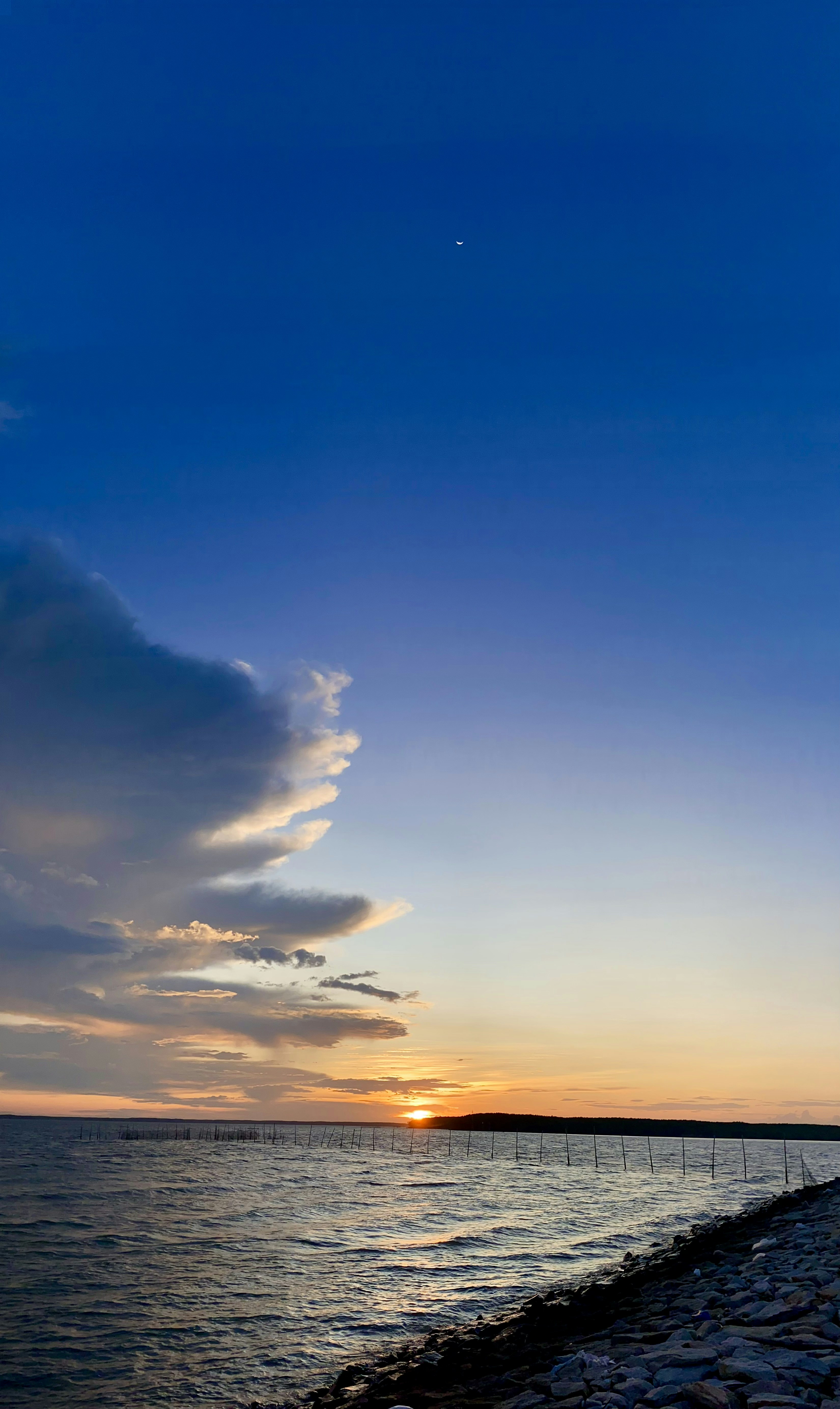 Golden sunset reflecting on tranquil waters, framed by distant clouds and a rocky shoreline.