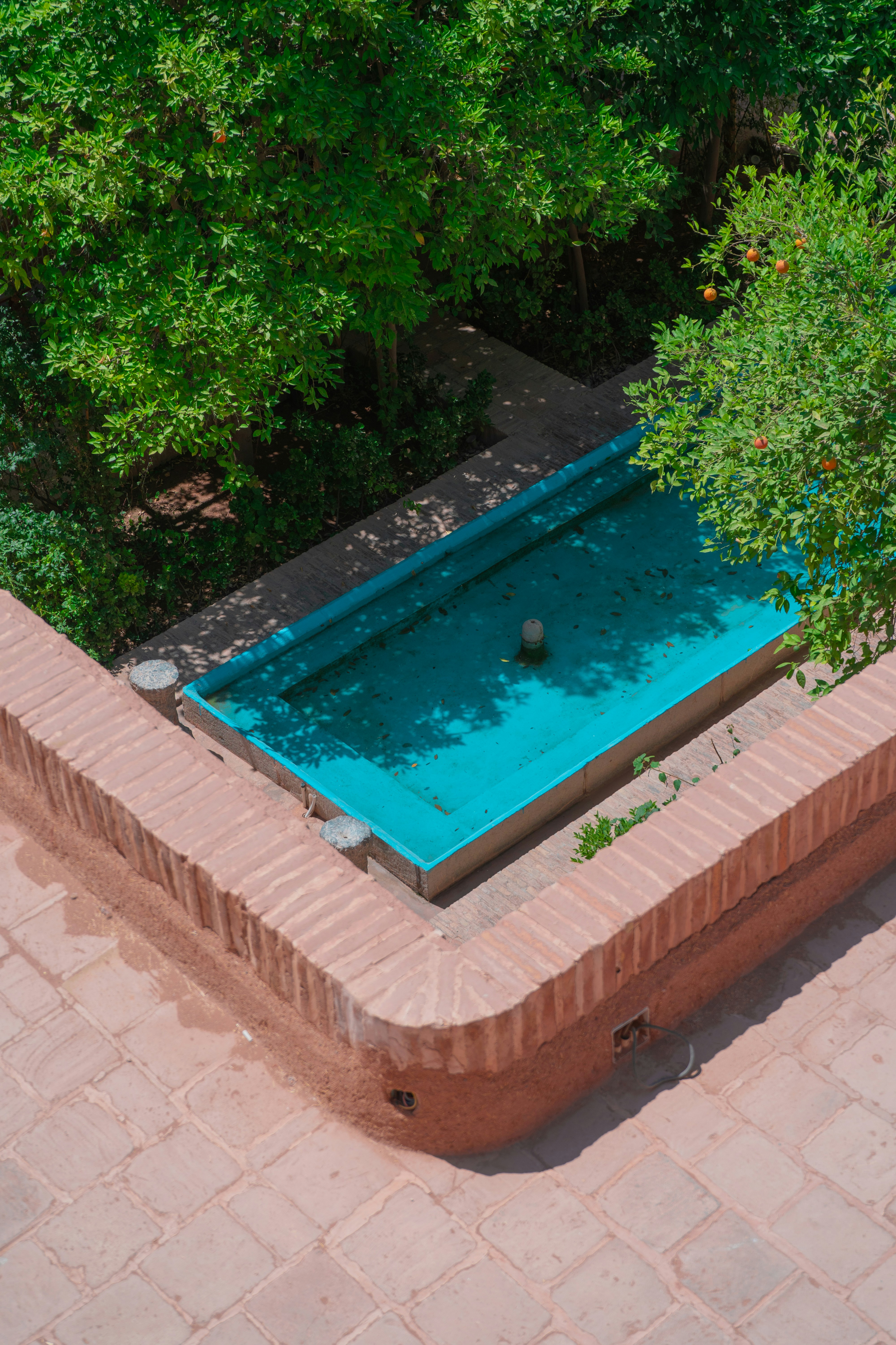 A serene blue fountain nestled among lush greenery, surrounded by terracotta walls and pathways.