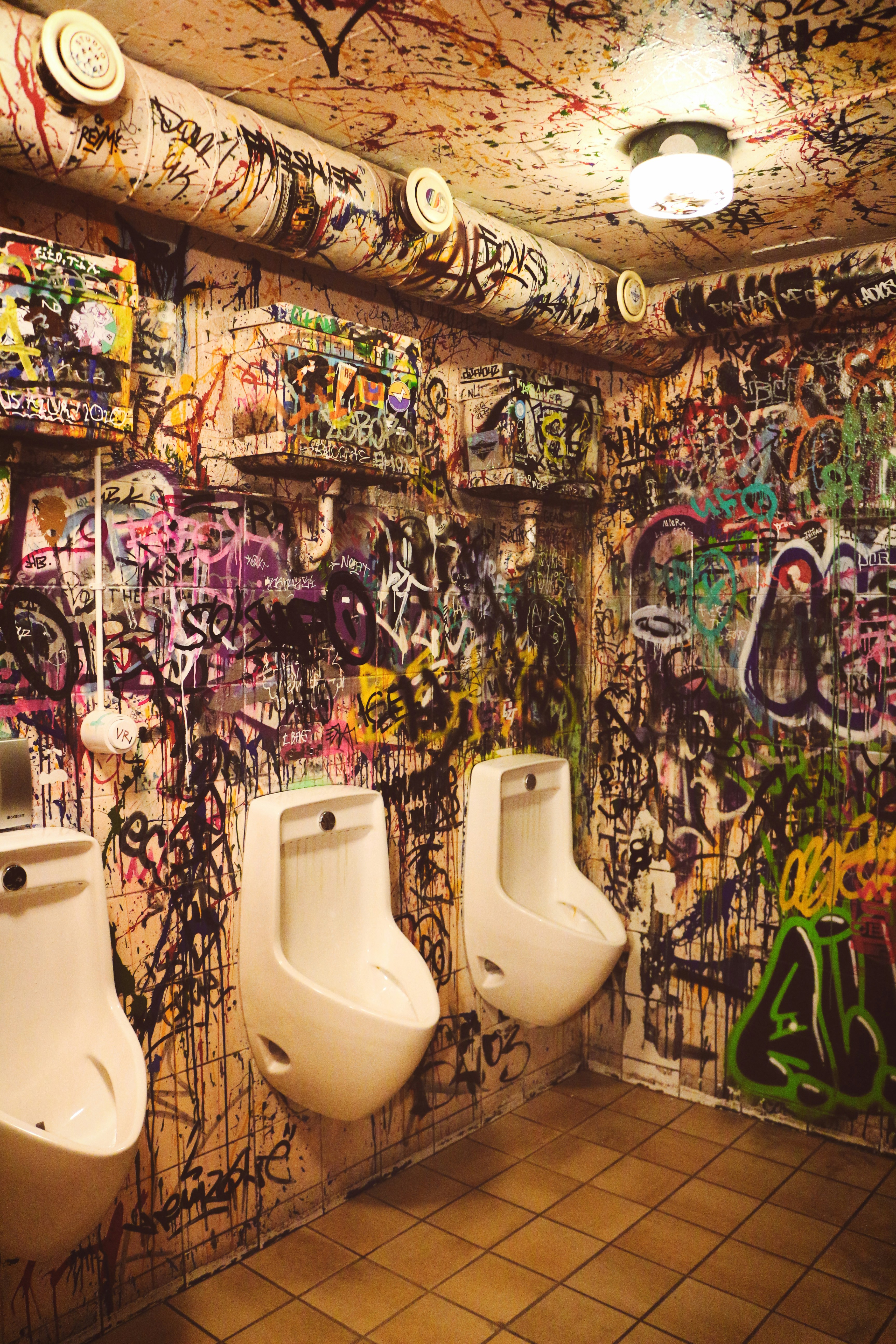 A bathroom with urinals covered in graffiti photo – Free Indoors Image ...