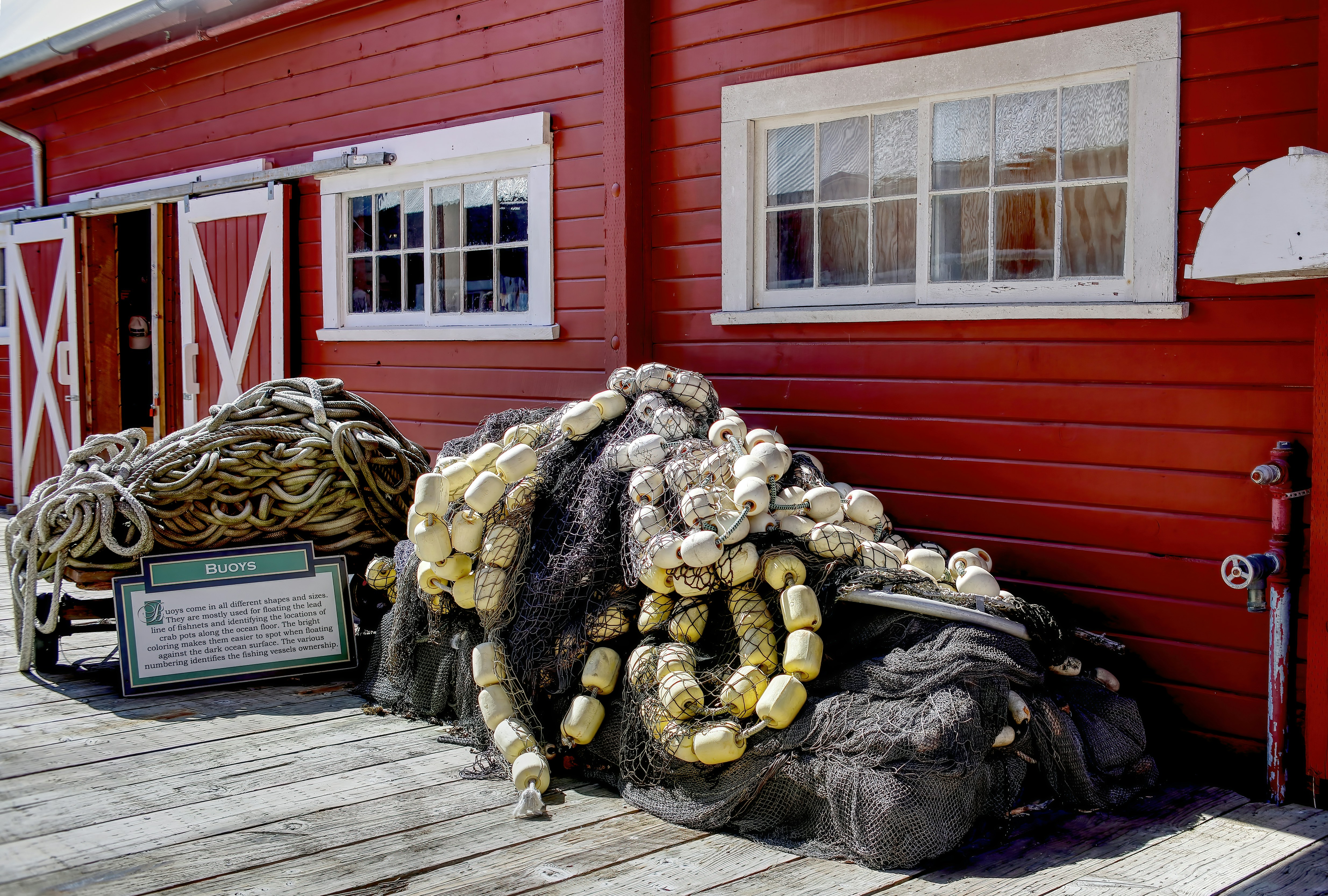 Colorful fishing gear piled against a vibrant red building, showcasing a blend of maritime history and craftsmanship.