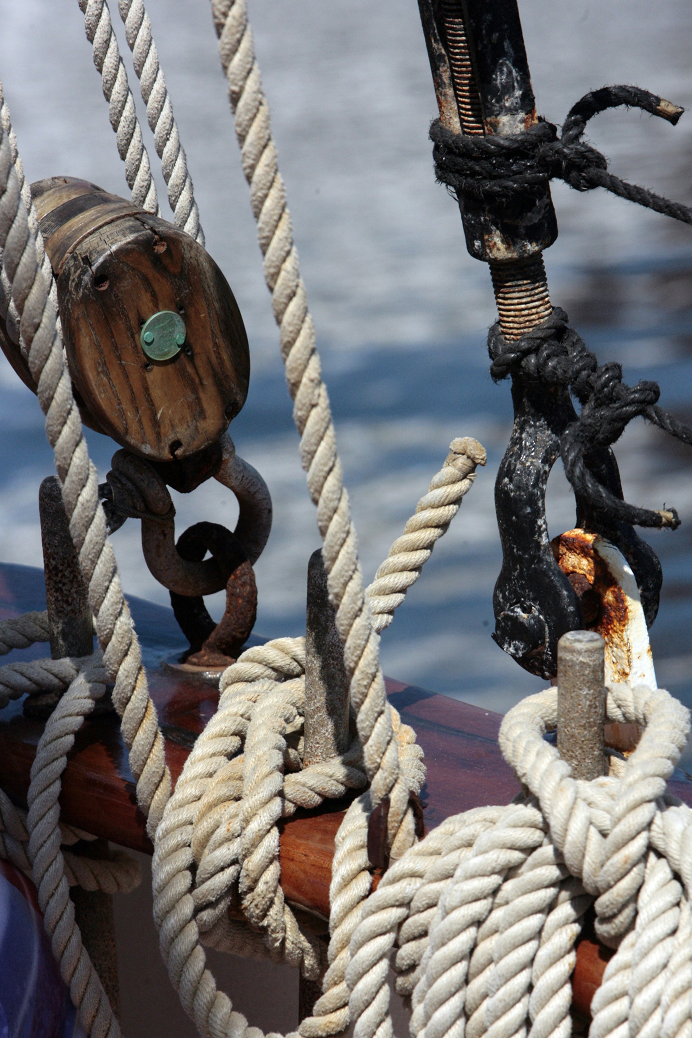 Close-up of ship rigging, showcasing wooden pulleys and intricate rope work against a shimmering water backdrop.