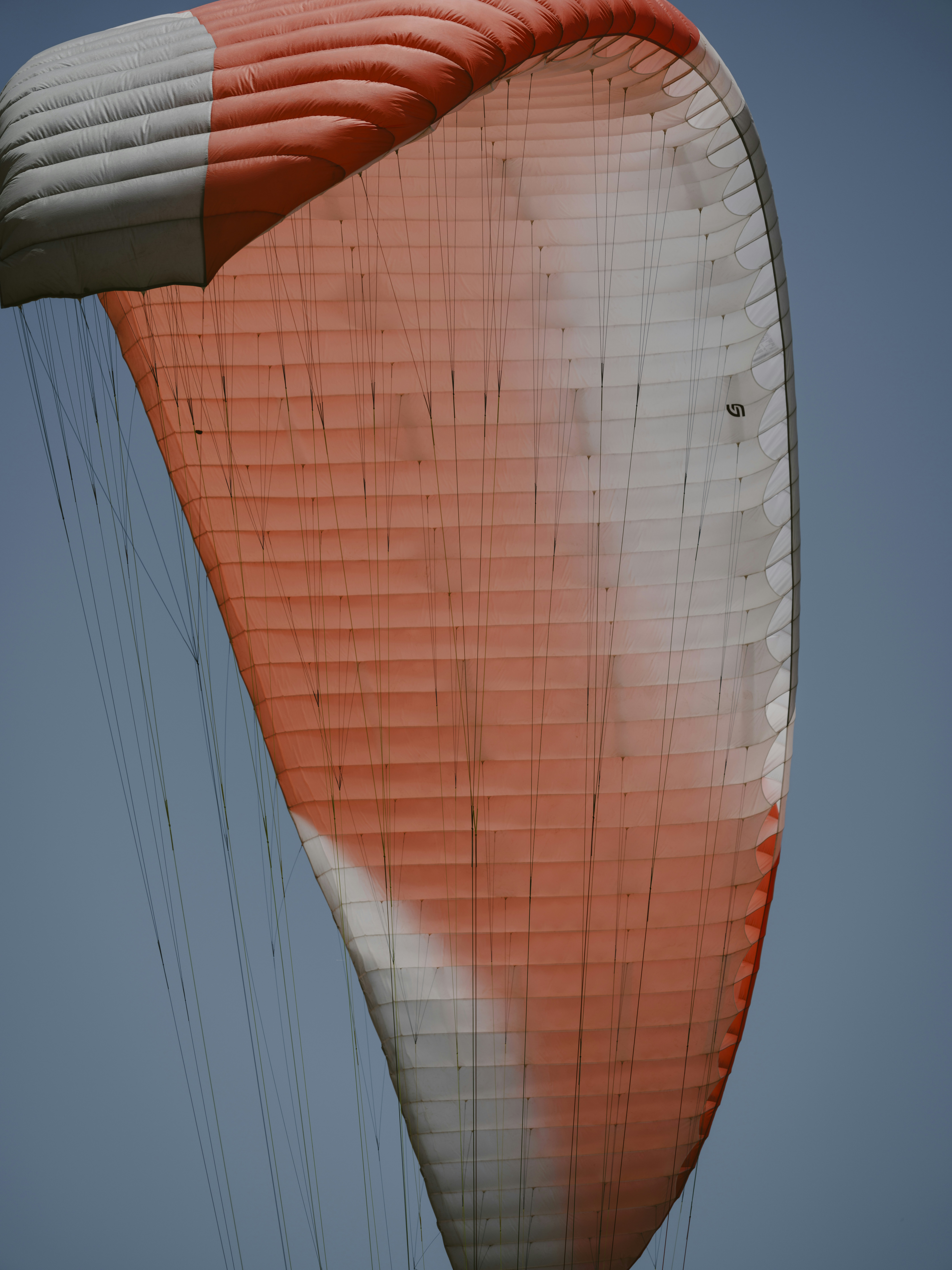Close-up of a vibrant orange and white paraglider soaring against a clear blue sky.