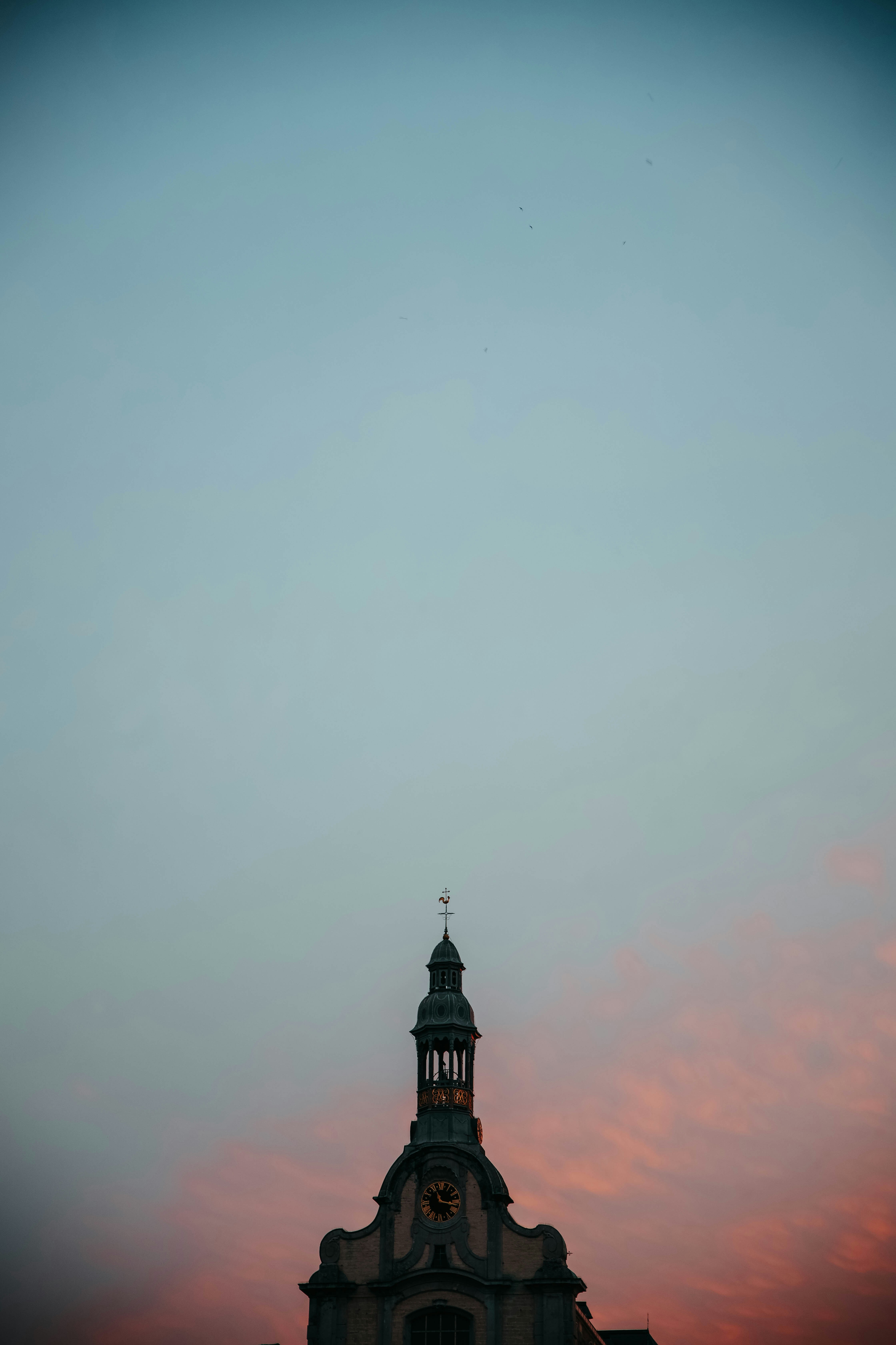 Historic building clock tower silhouetted against a pastel twilight sky, showcasing architectural elegance. 