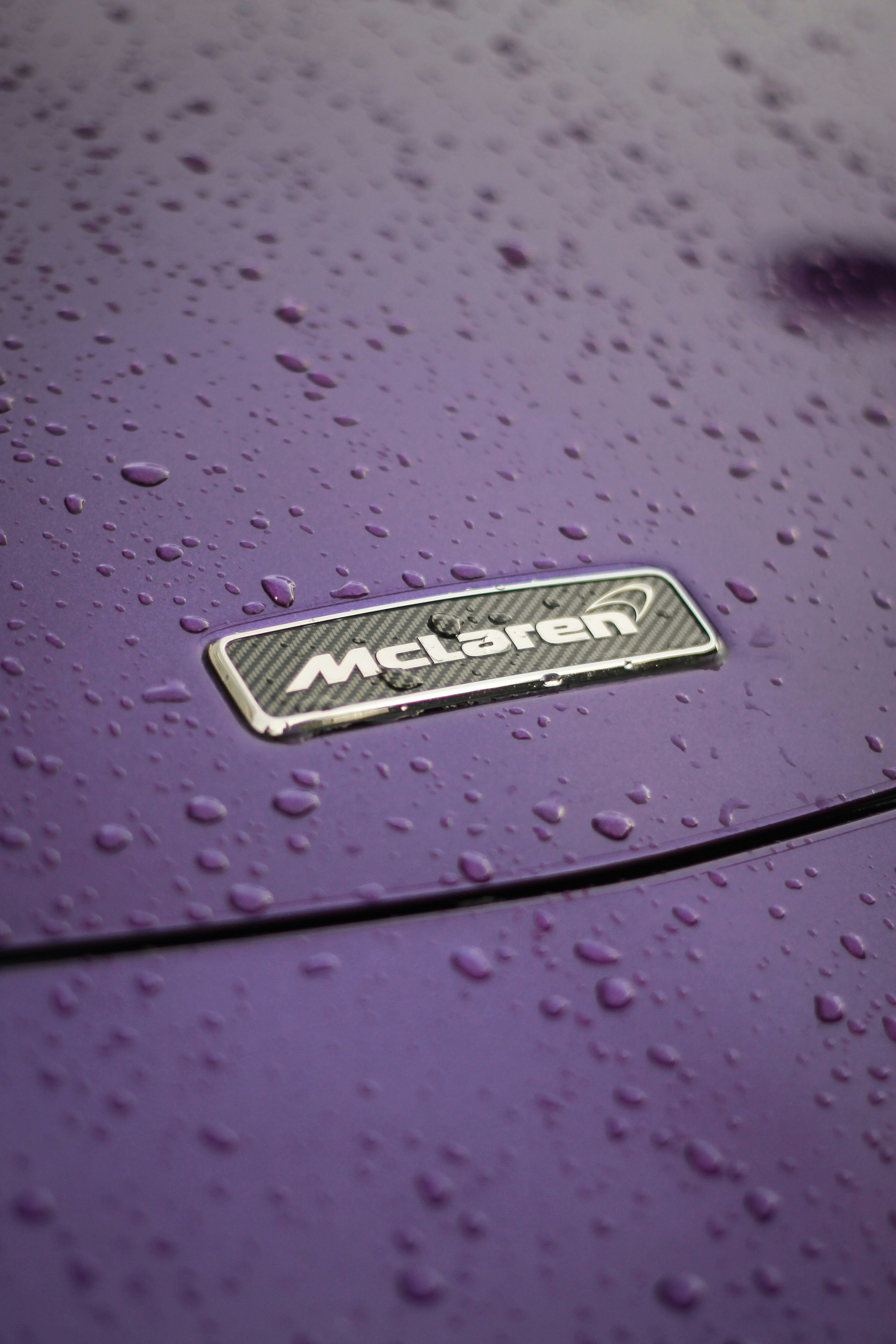 Purple McLaren Badge Glinting Through Rain Droplets