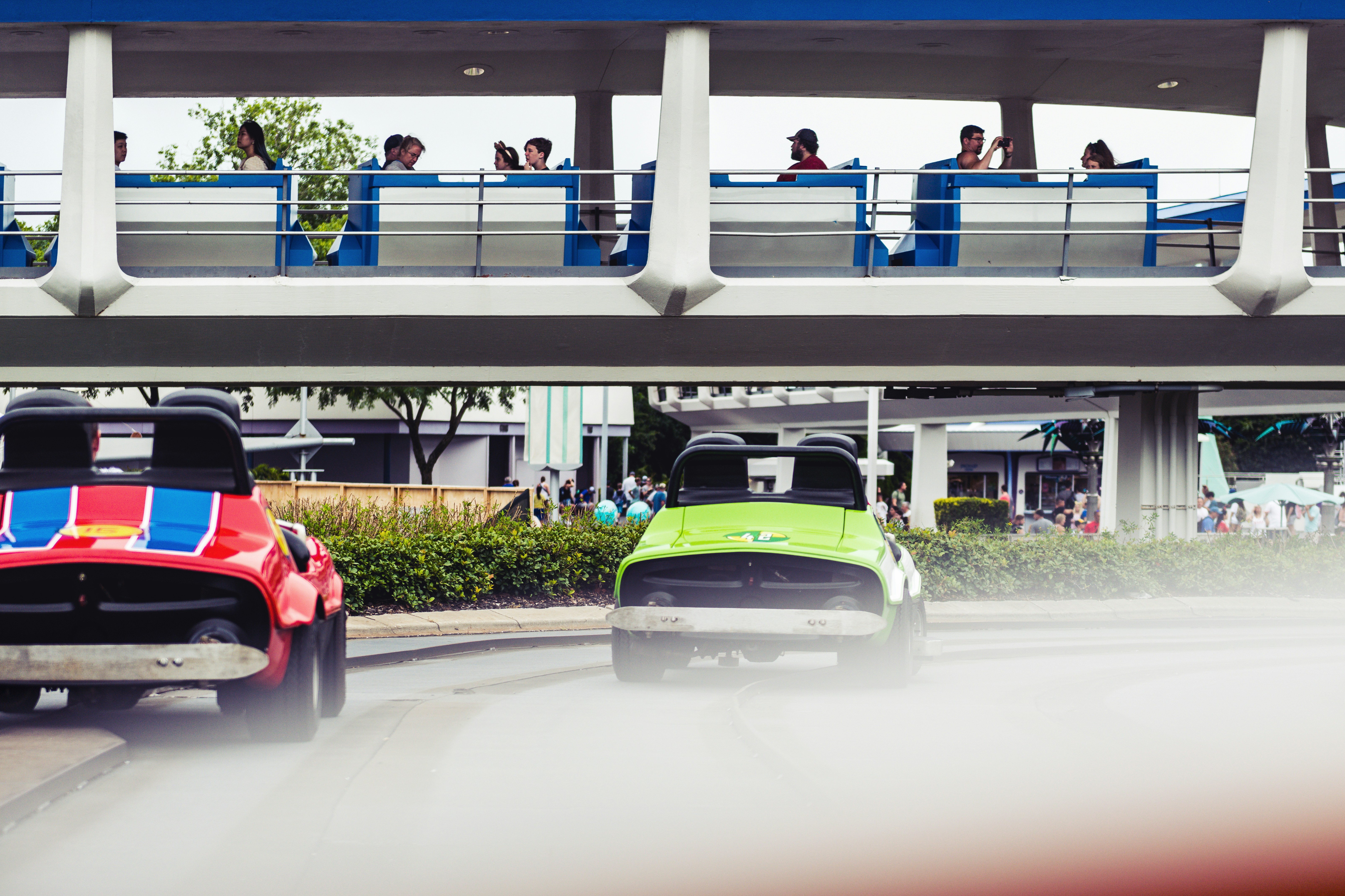 Colorful cars on a track beneath a futuristic monorail at a theme park.