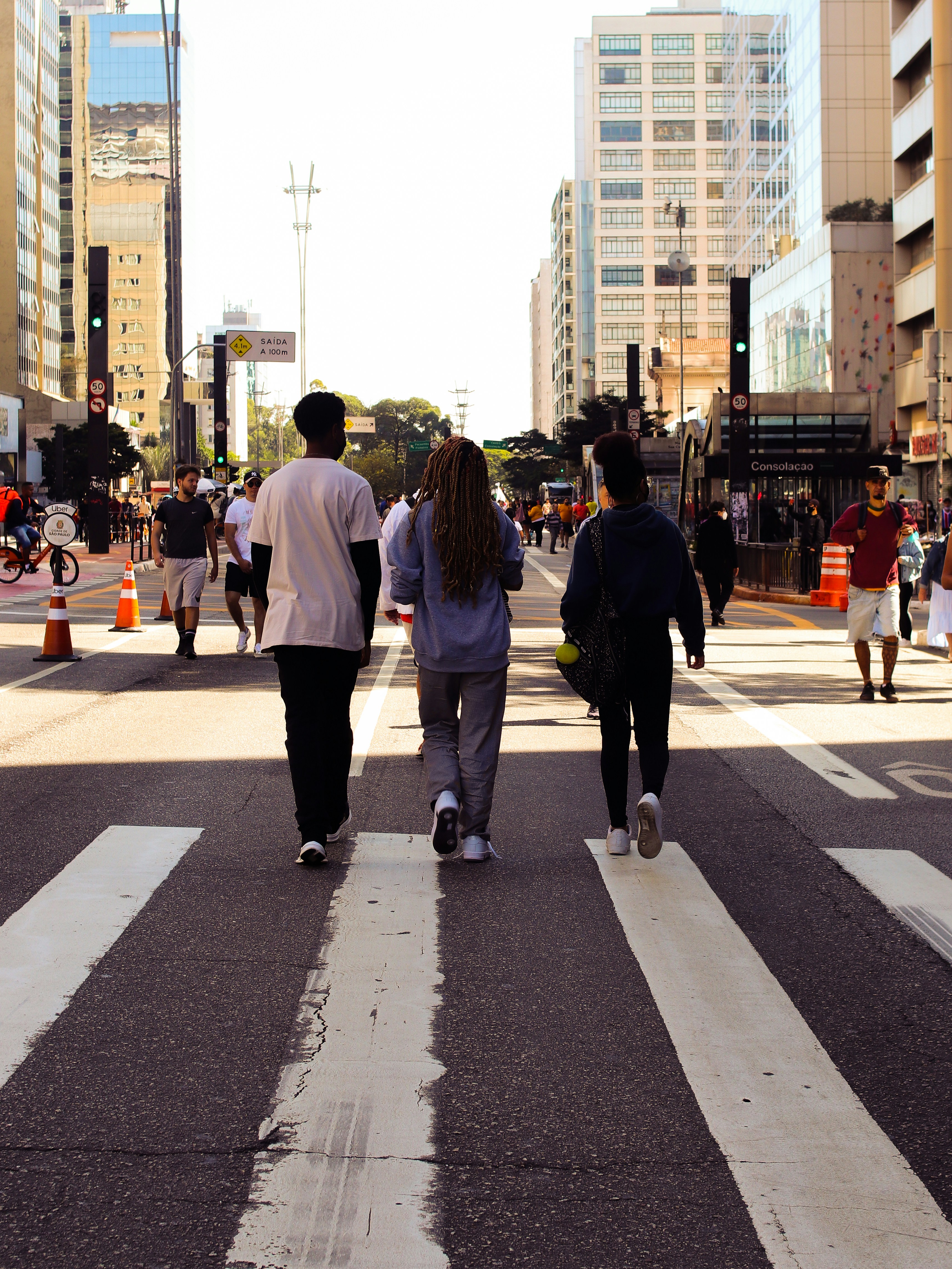 Crosswalk Trio: Three Pedestrians Stepping Through a Sunlit Downtown Crossing