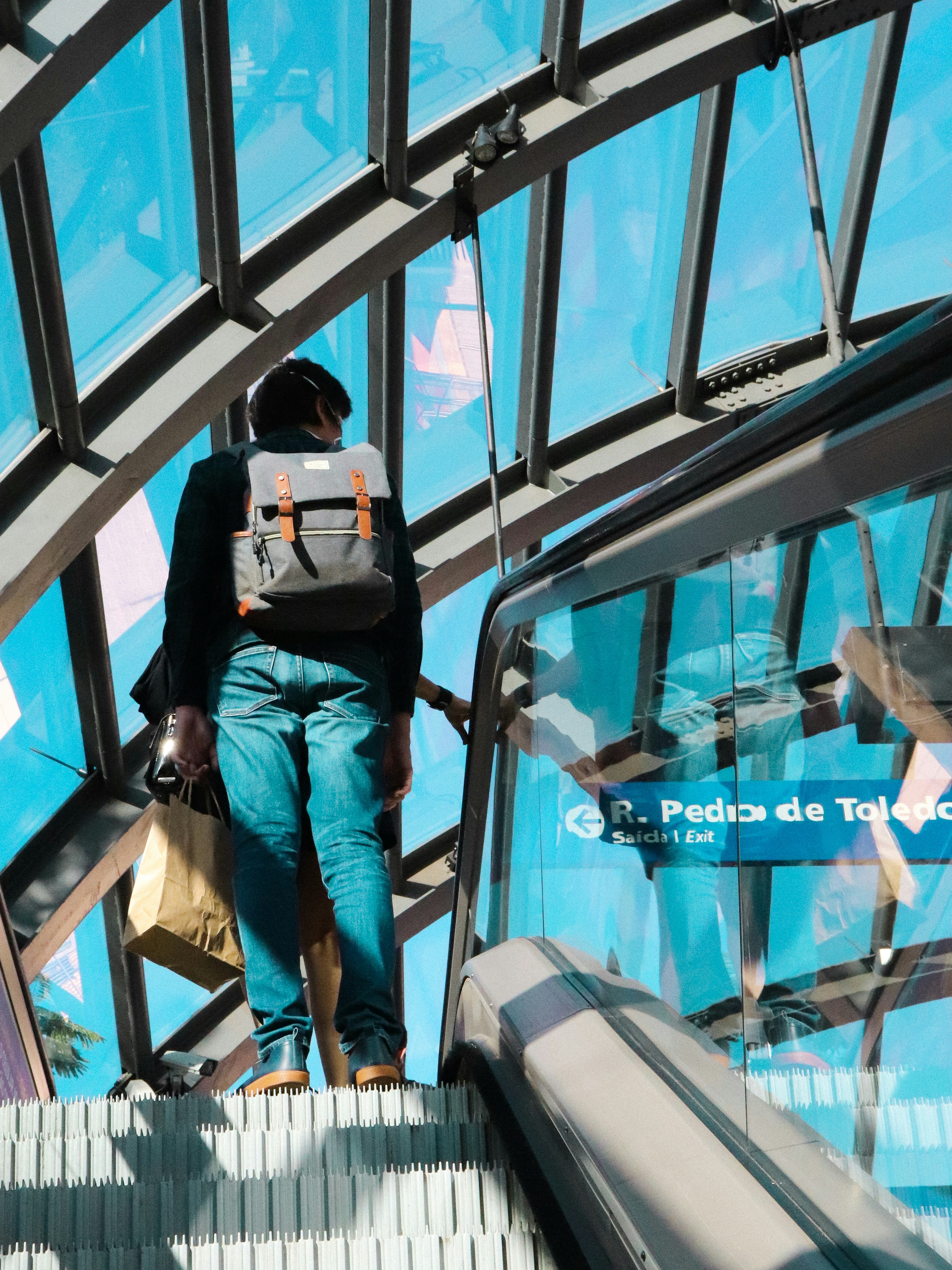 Escalator in the Glass Atrium: A Backpacker Steps into the Light