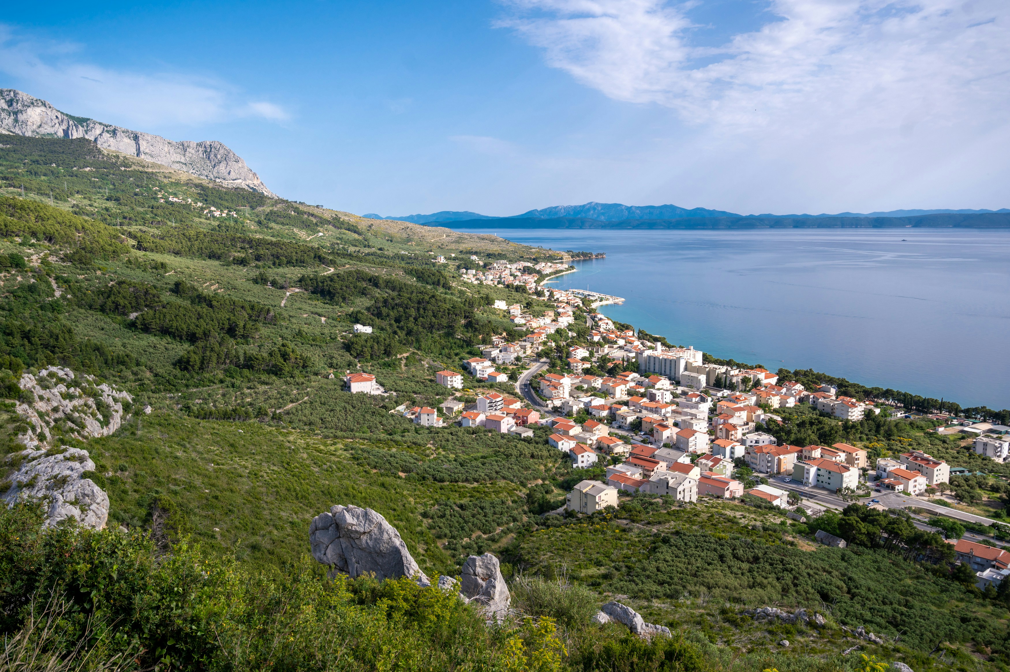 A picturesque coastal village nestled between lush hills and the serene Adriatic Sea, showcasing a blend of natural beauty and human habitation.