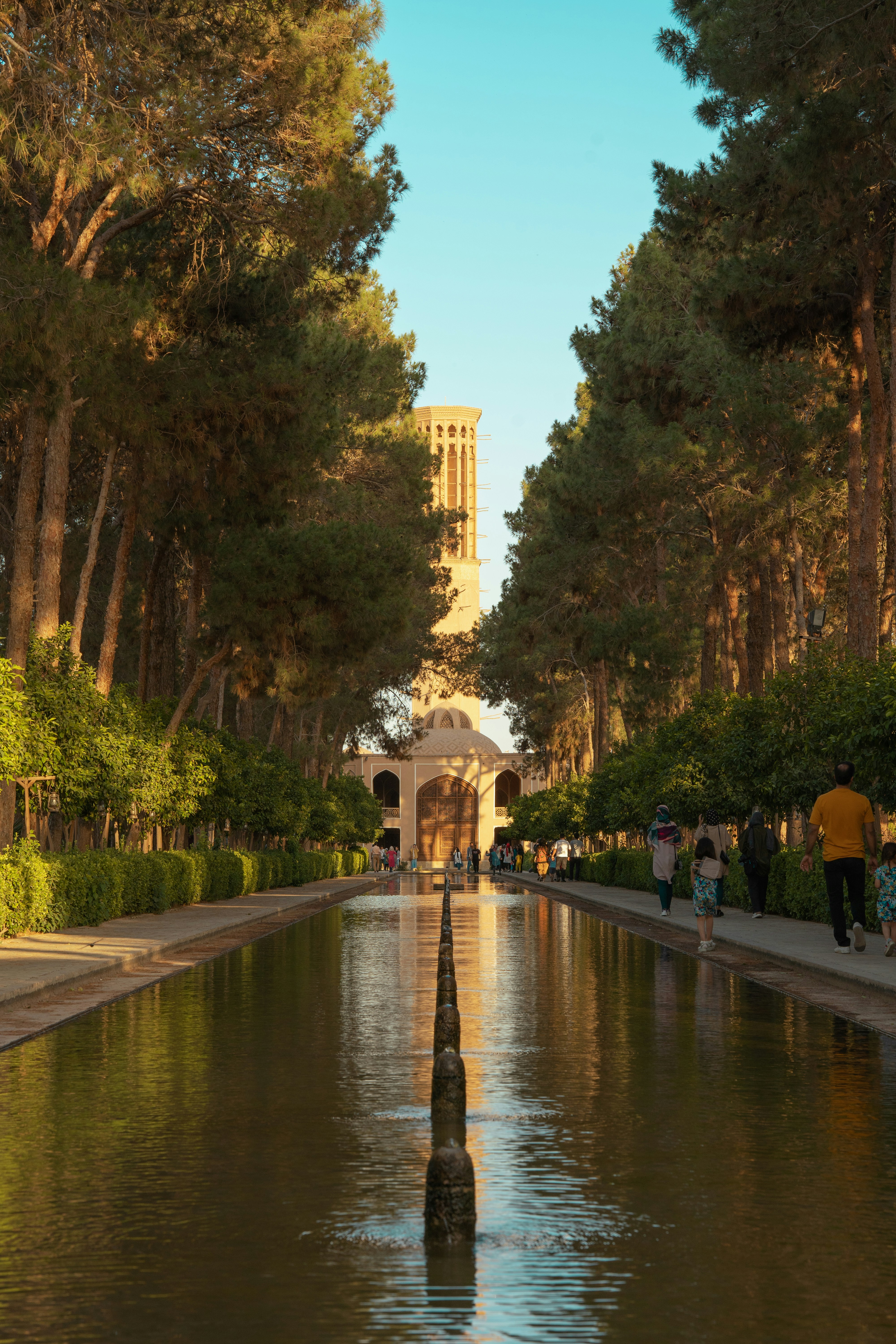 Symmetrical pathway lined with lush trees and a tranquil water feature leading to an architectural marvel in the background.