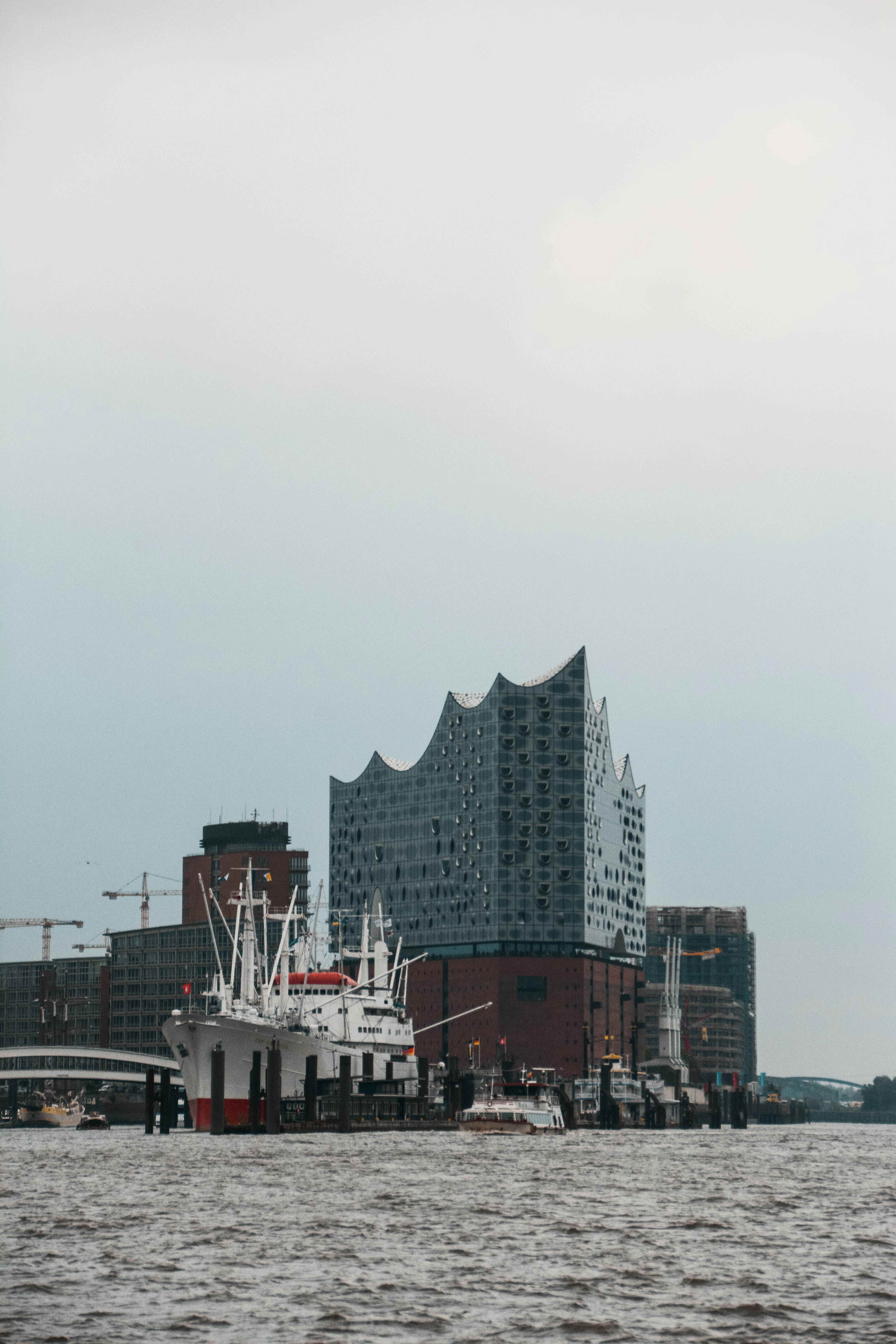 A striking modern architectural marvel alongside traditional vessels docked in a bustling harbor. The scene captures the blend of old and new in an urban waterfront setting.
