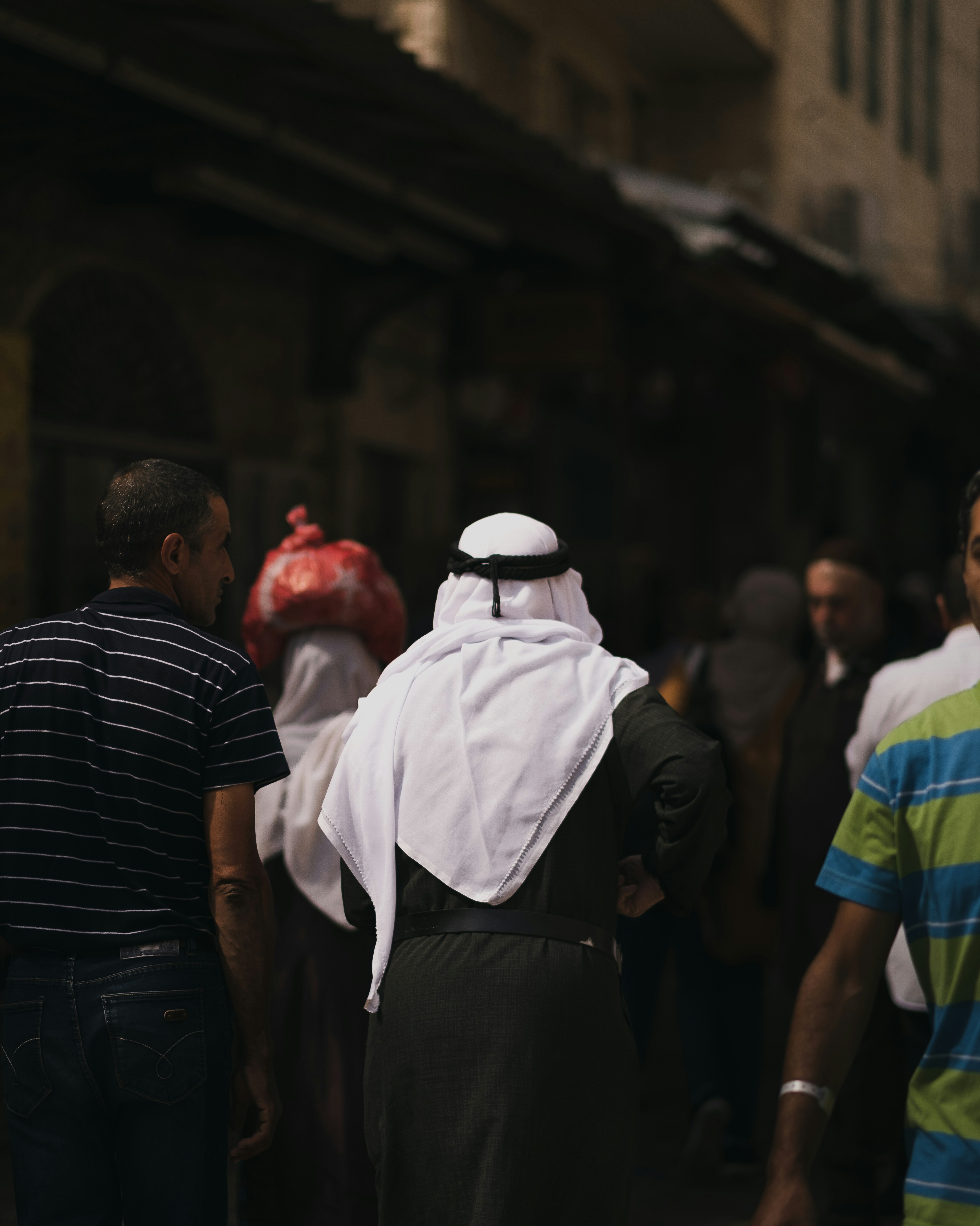 A diverse group of individuals navigating a bustling market street, showcasing traditional attire amidst a vibrant urban backdrop.