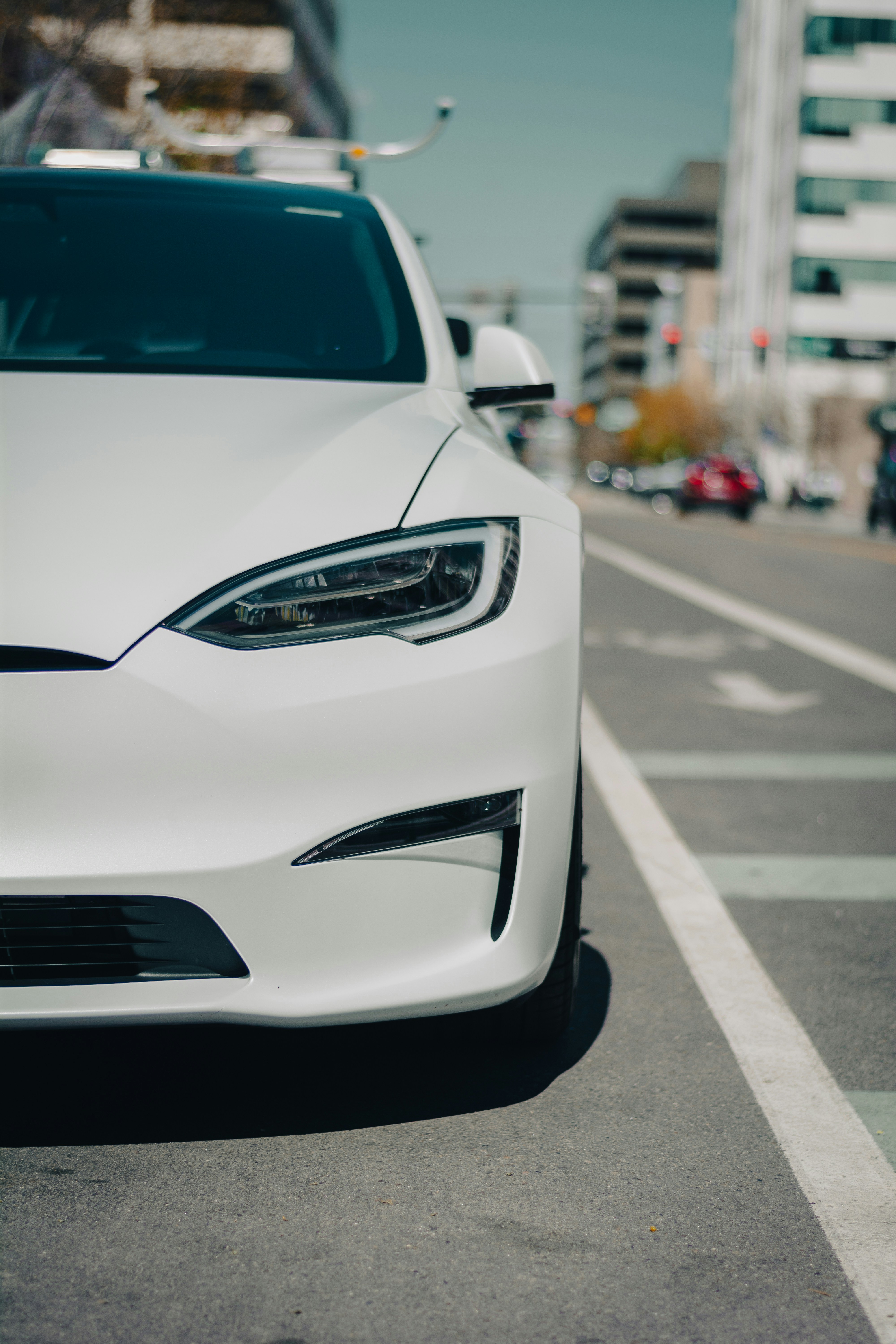 Front view of a white electric car parked on a city street, showcasing its sleek design and futuristic headlights.