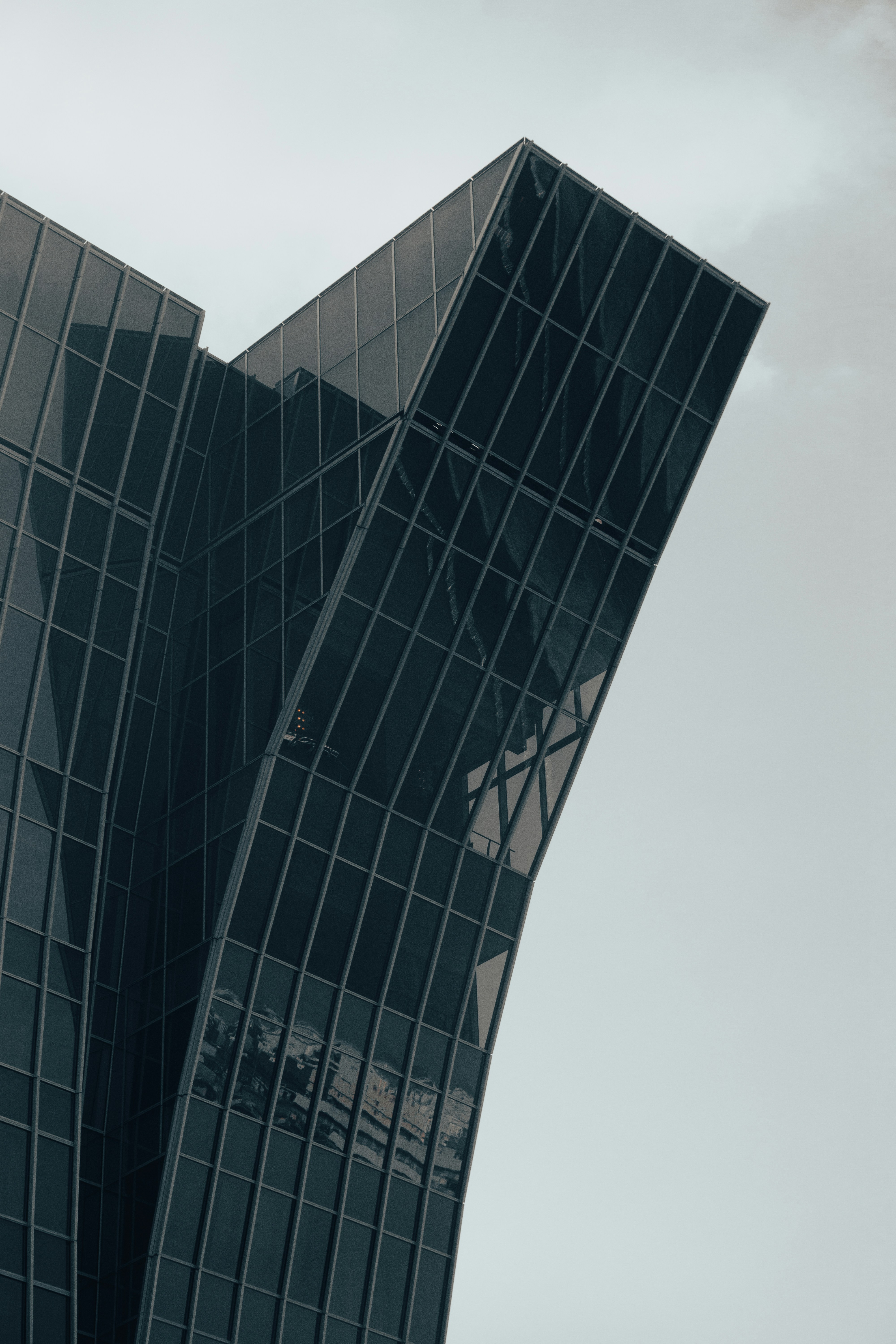 Dynamic glass structure with angular facets reflecting the sky, showcasing contemporary architectural design.