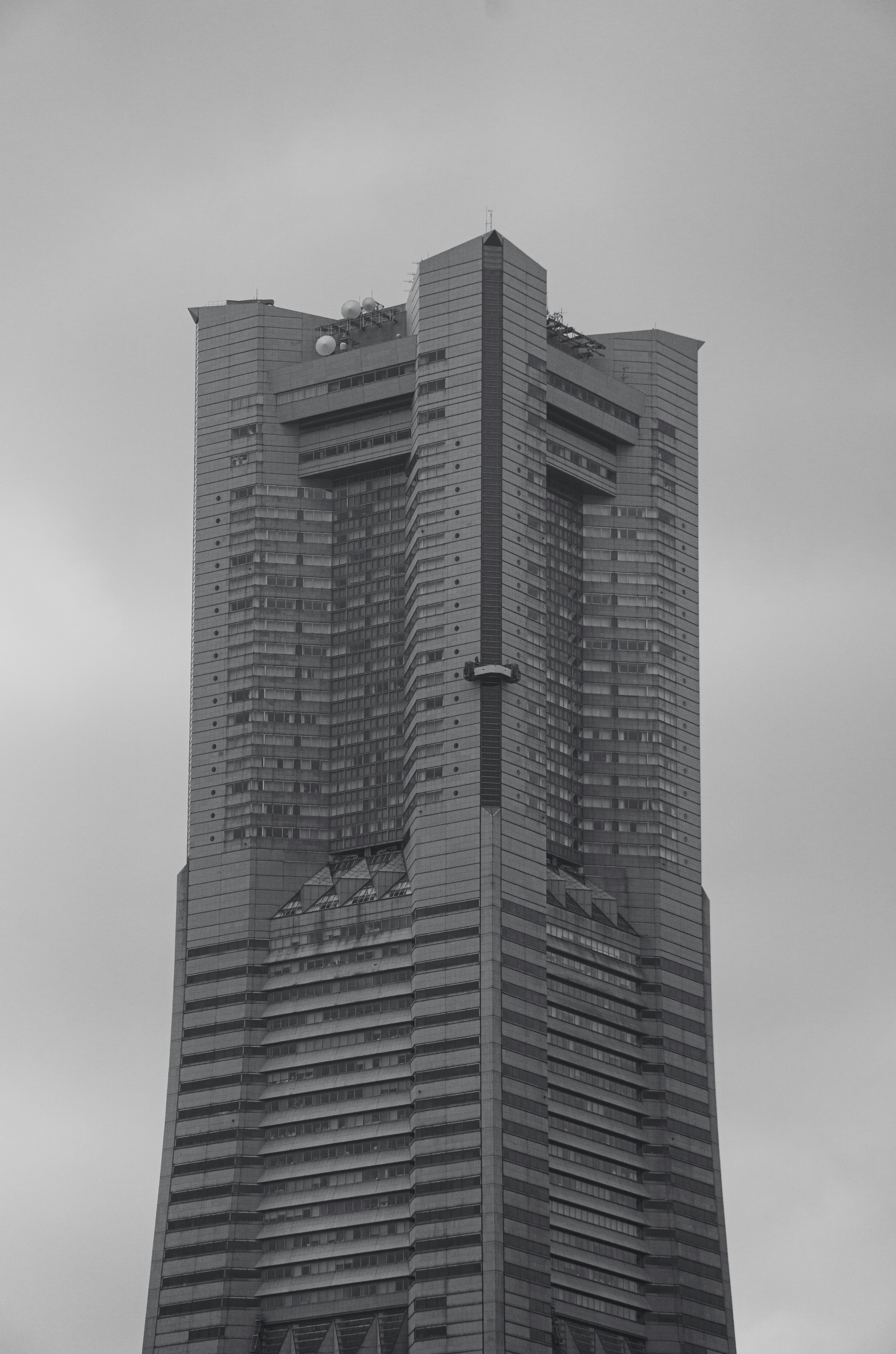 A towering skyscraper showcases its sleek architecture against a cloudy sky, highlighting the interplay of glass and metal. The structure's design emphasizes vertical lines and geometric patterns.