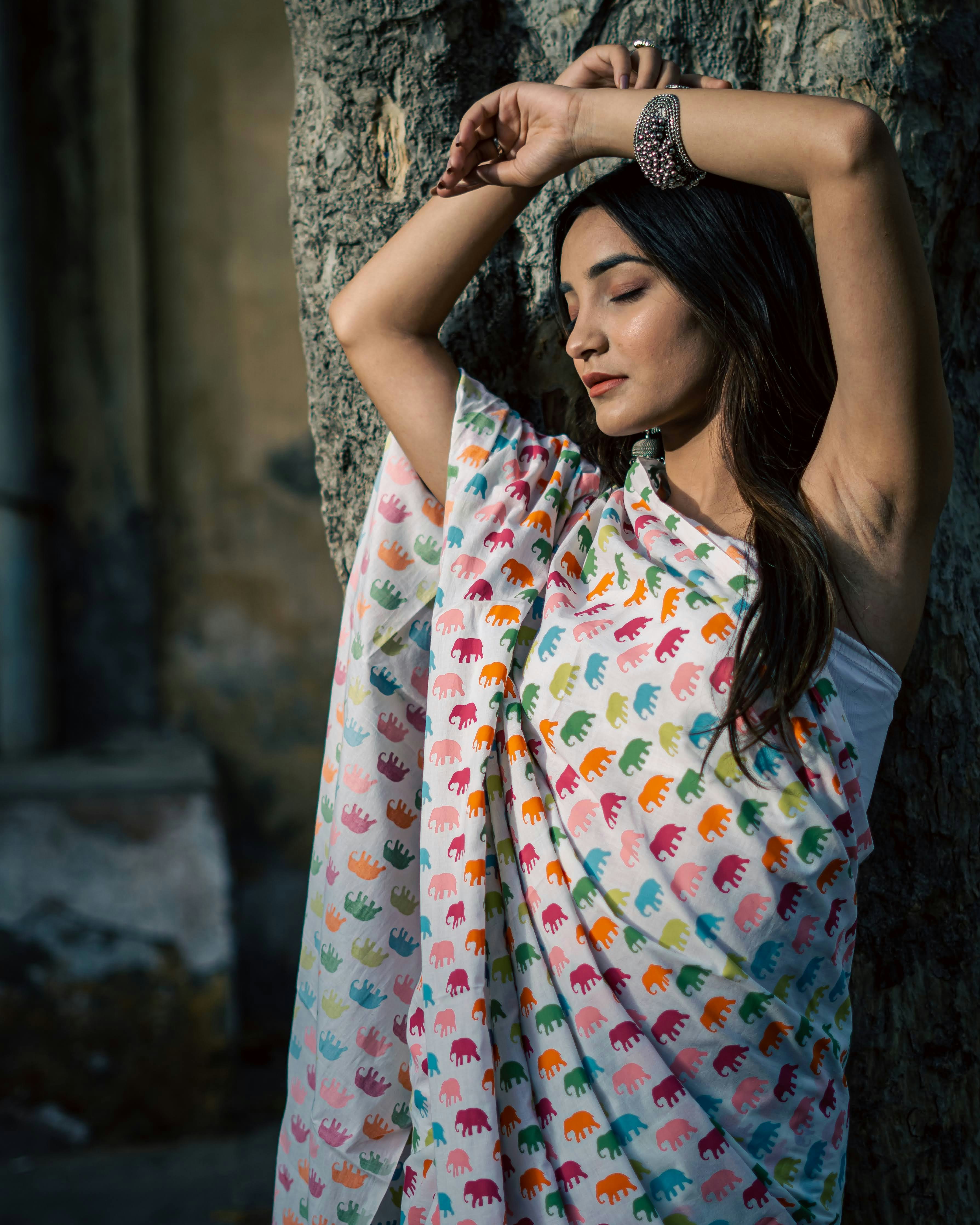 Portrait photograph of a woman resting against a textured tree trunk, wrapped in a colorful elephant-pattern shawl.