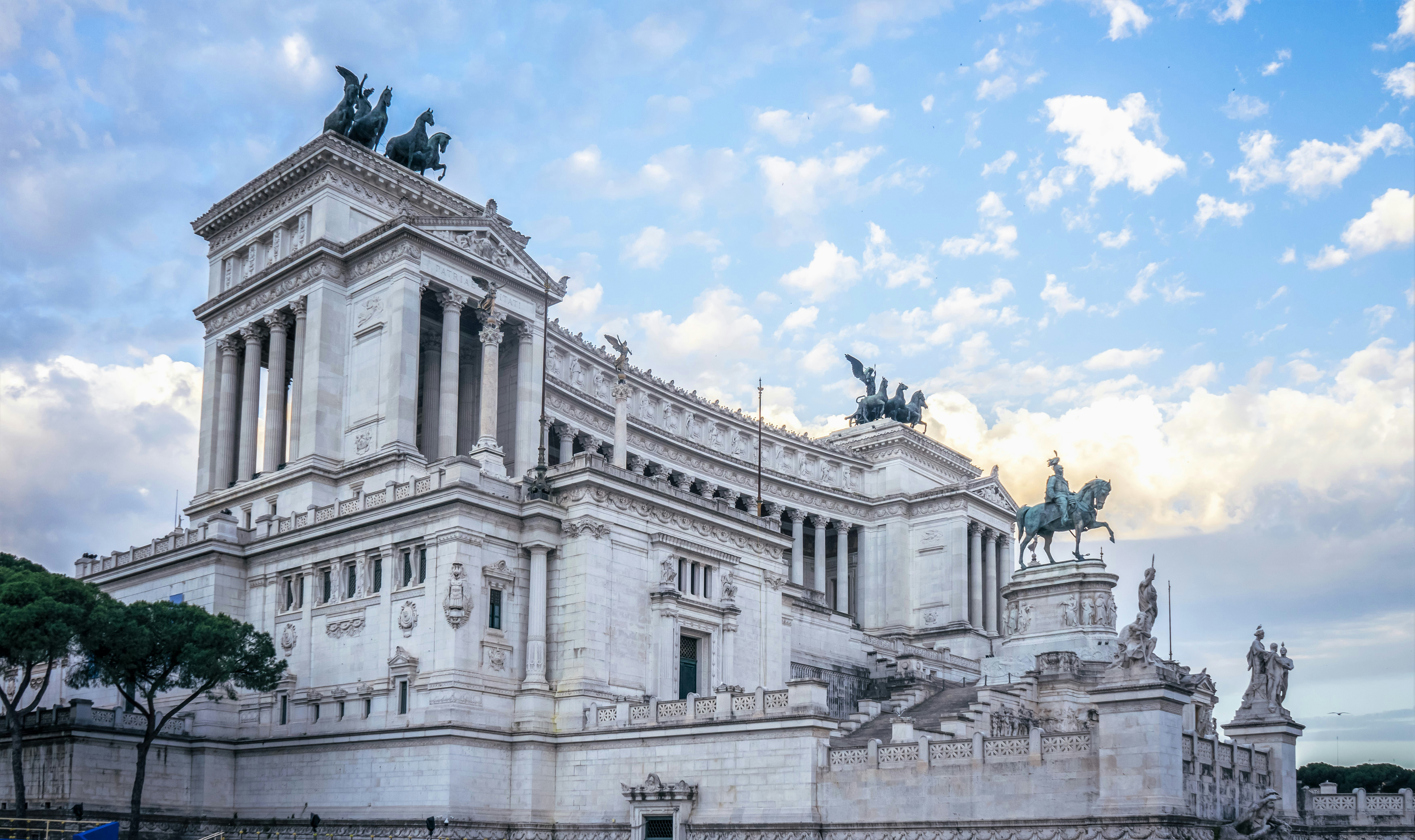 Imposing white marble monument featuring grand sculptures and a dramatic sky backdrop. The structure showcases classical architecture and historical significance.