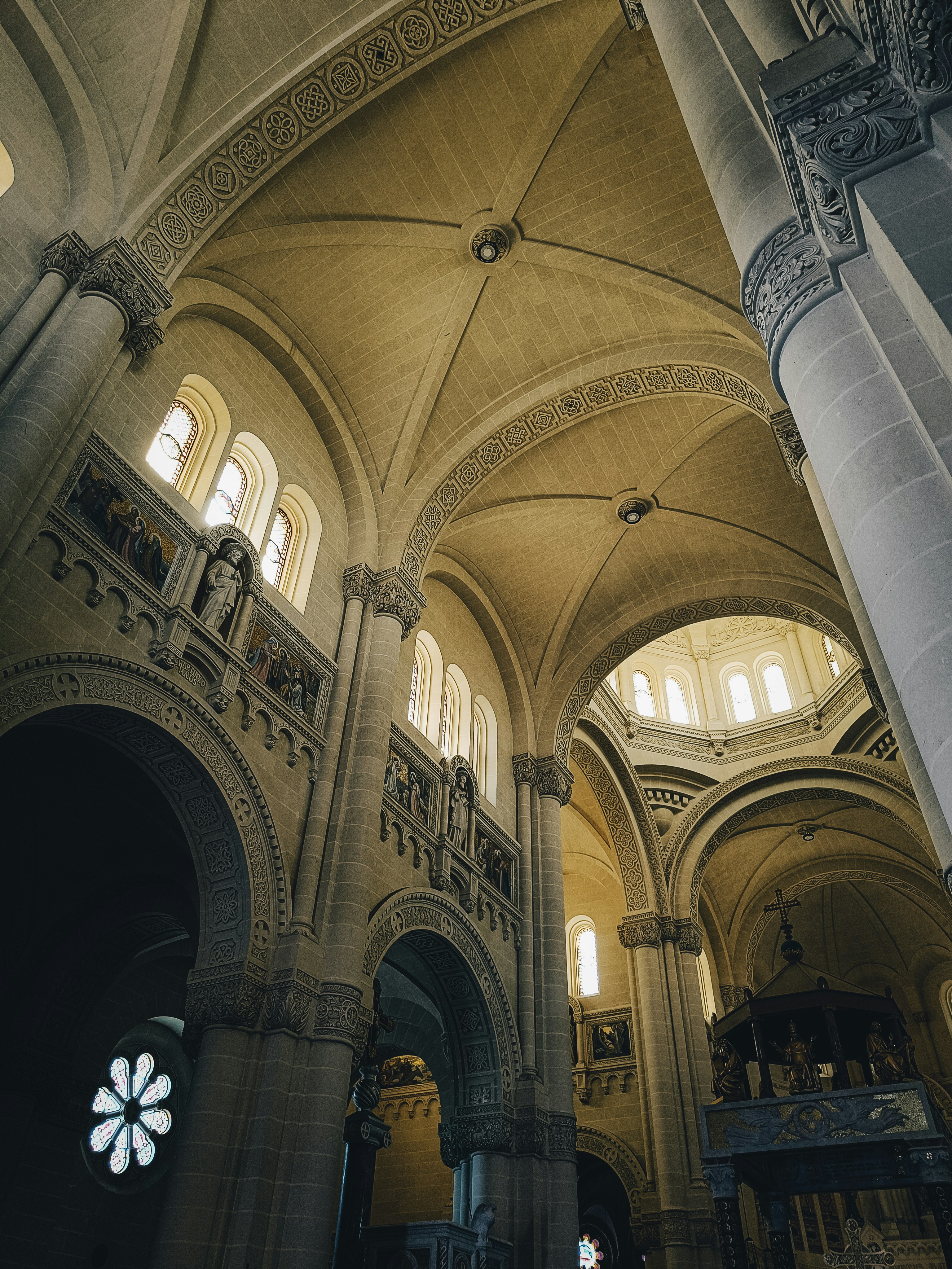Intricate vaulted ceilings and arched windows illuminate the serene interior of a historic church, showcasing detailed craftsmanship and spiritual ambiance.