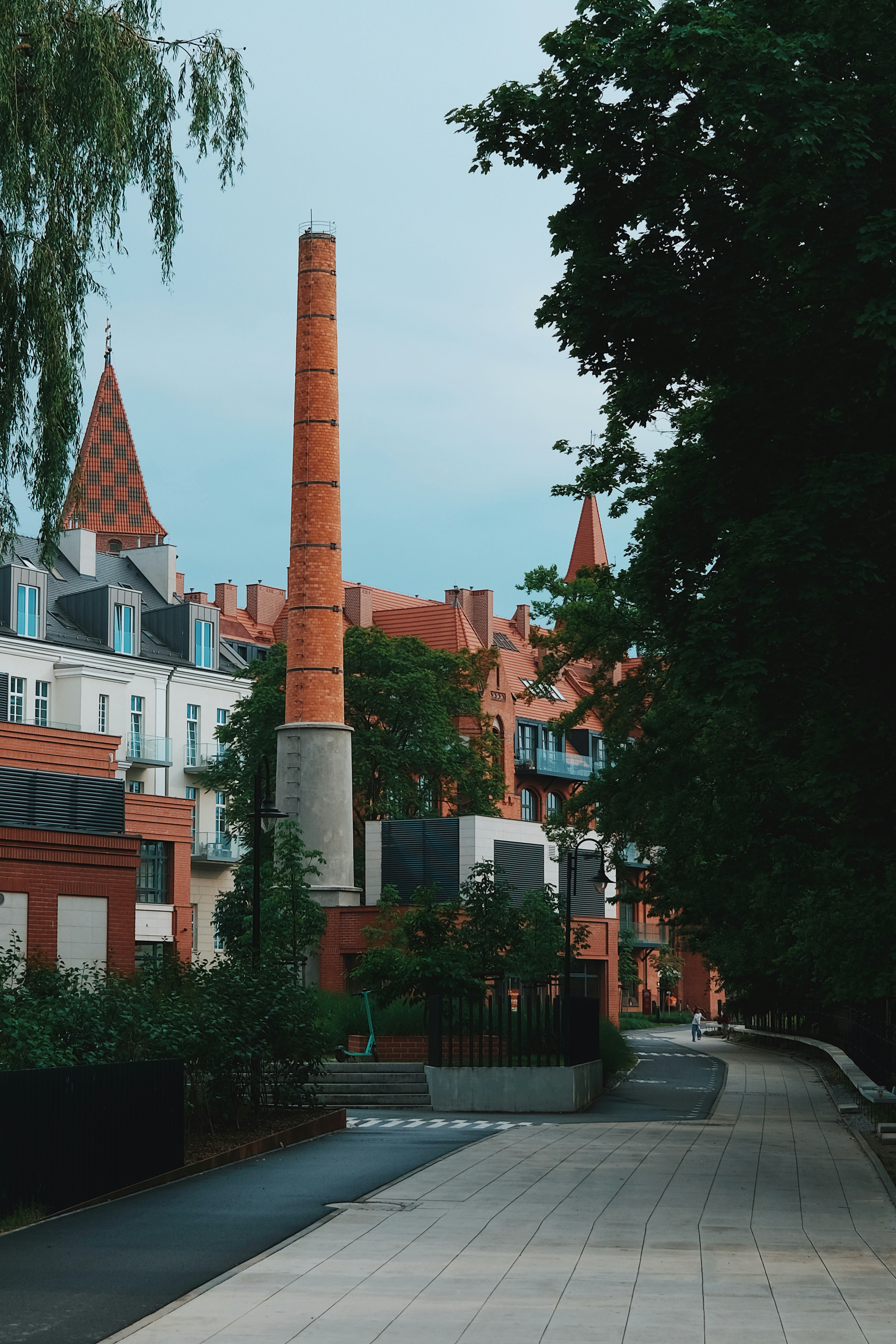 Chimney Rising Over Red-Tiled Cityscape on a Quiet Tree-Lined Street