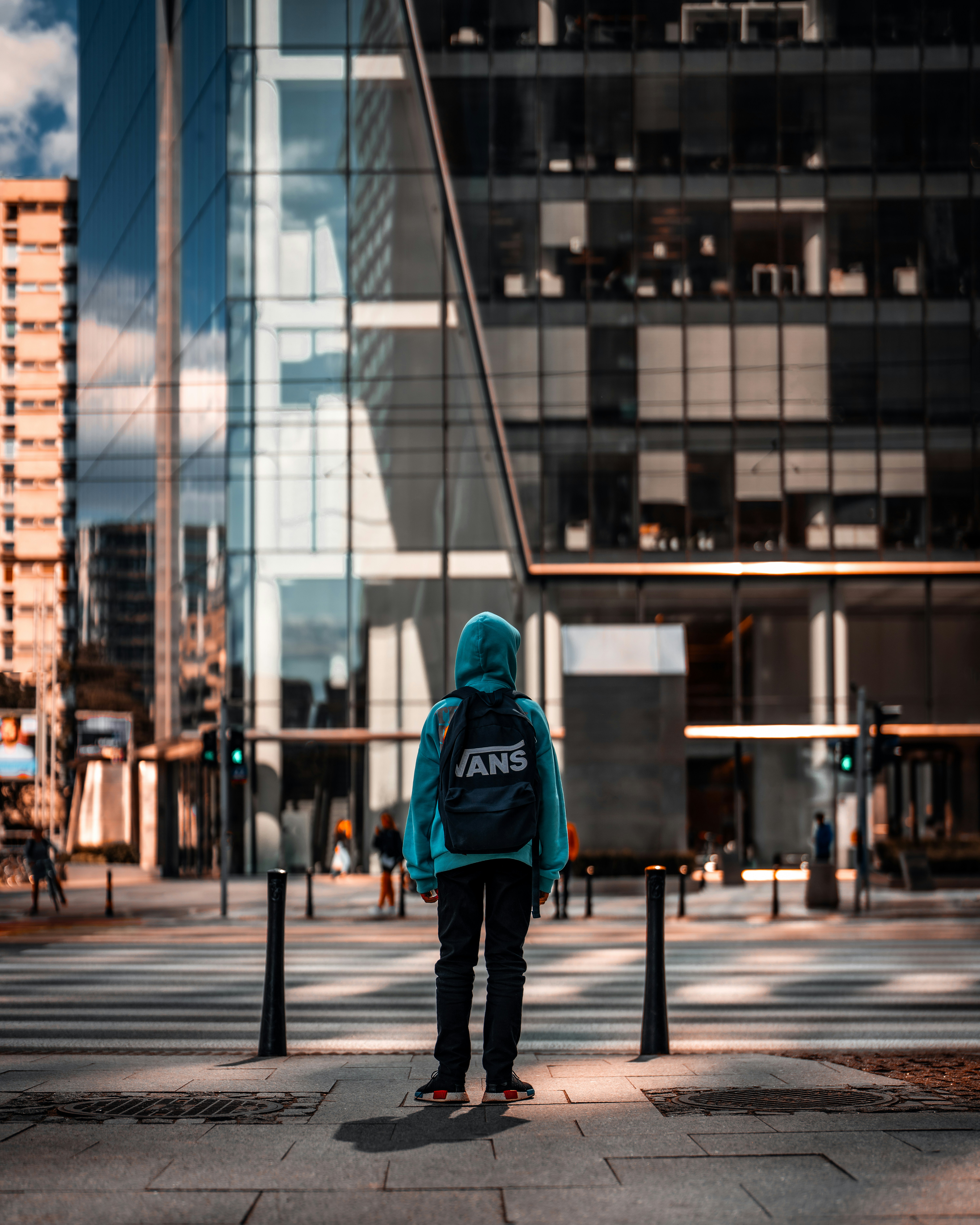 Hooded Figure at the Glass Canyon: A Quiet Crossing in Urban Light