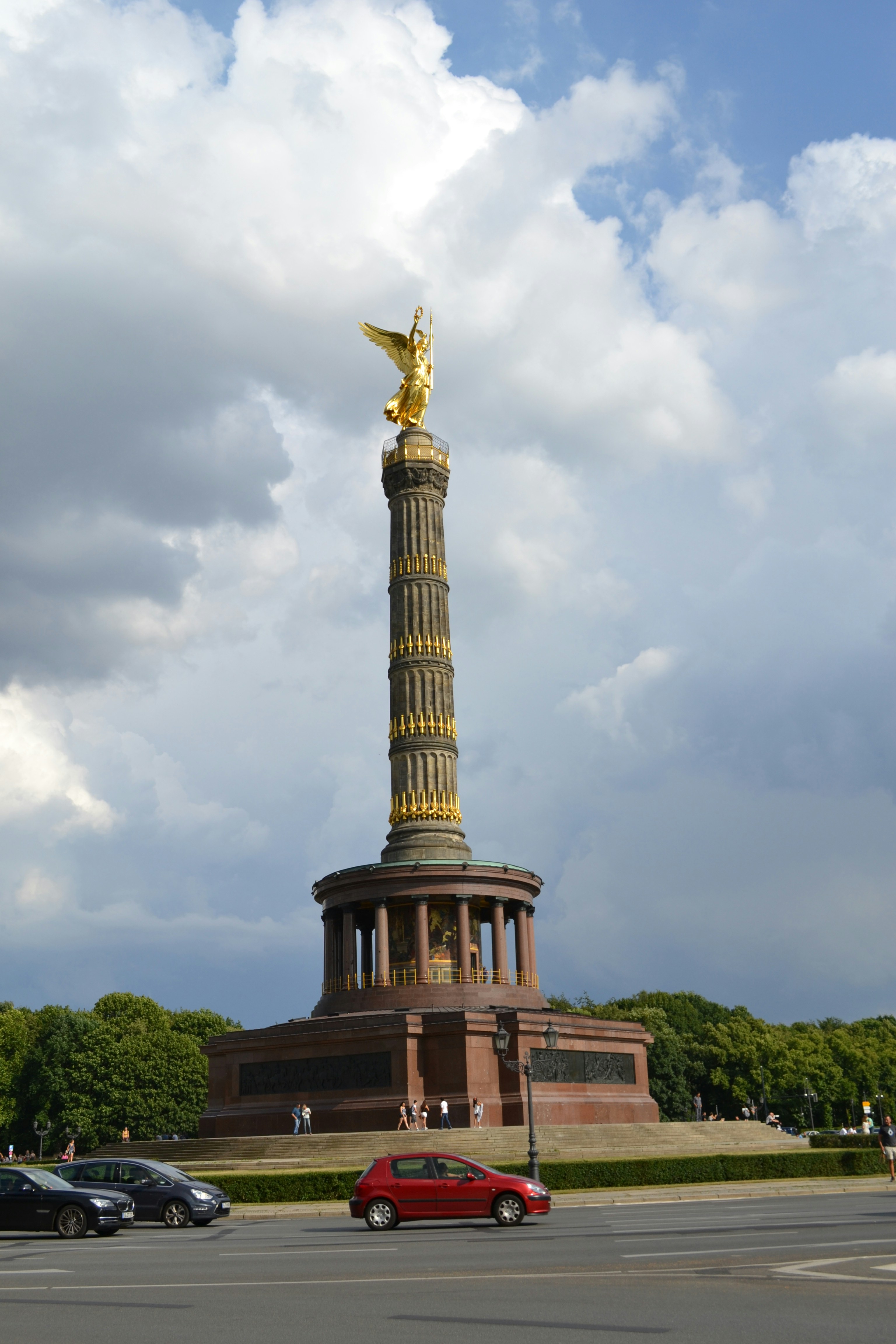 Victory Column stands tall against a backdrop of dynamic clouds, showcasing its intricate architecture and golden statue. The monument symbolizes triumph and resilience.