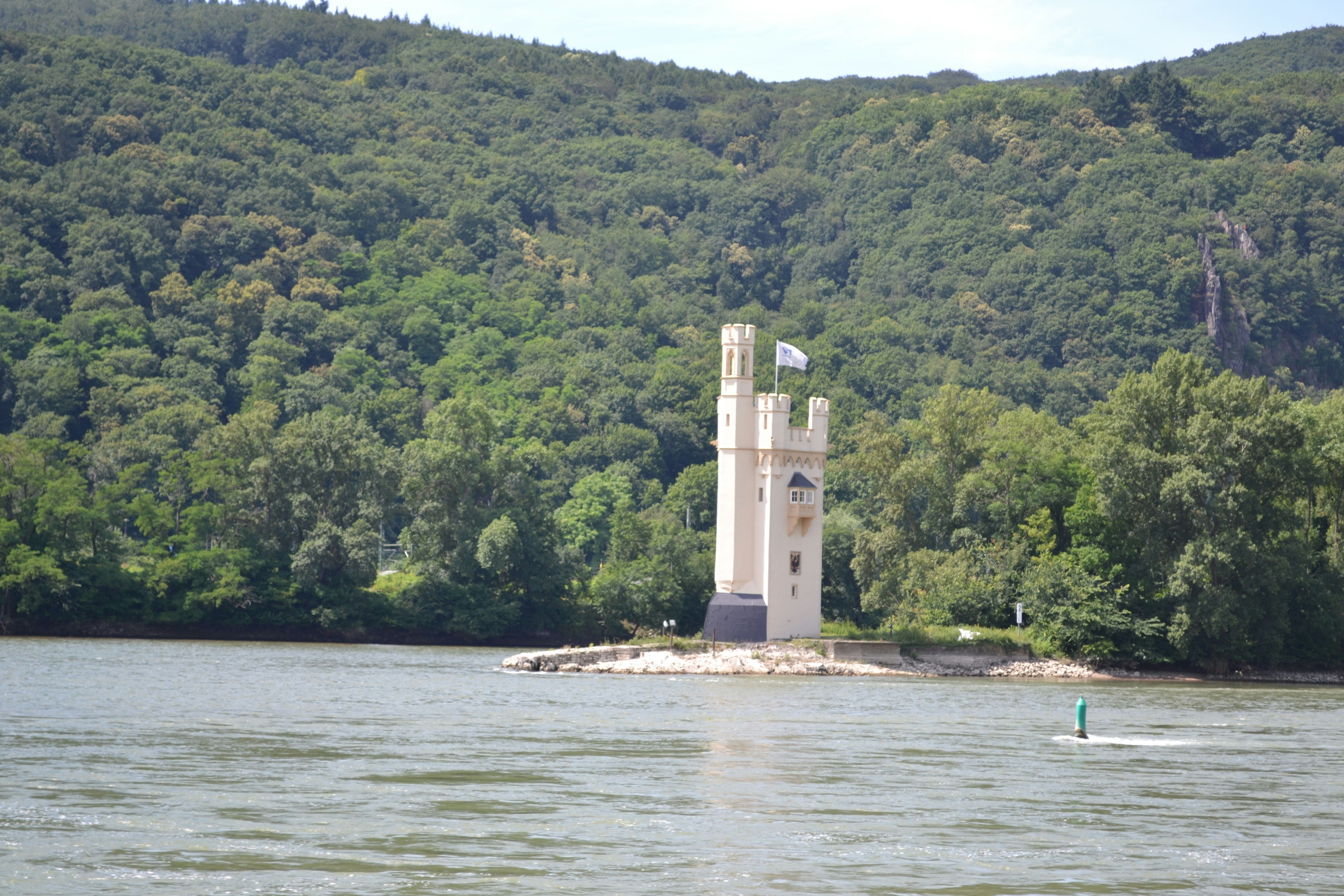 Historic tower standing on a small river island surrounded by lush green hills and serene waters.