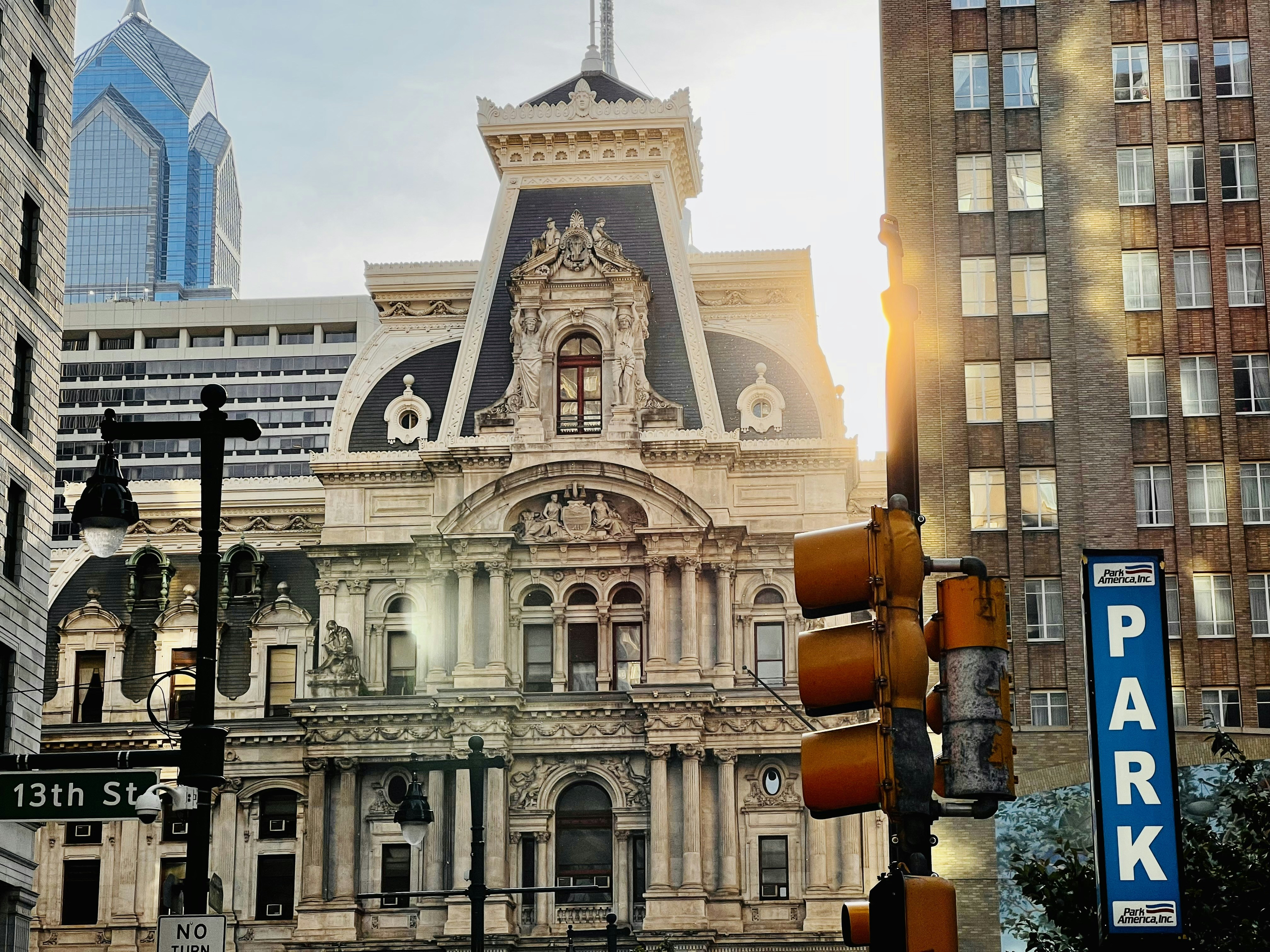 Ornate architecture of Philadelphia's city hall with a clock, framed by urban buildings at sunset.