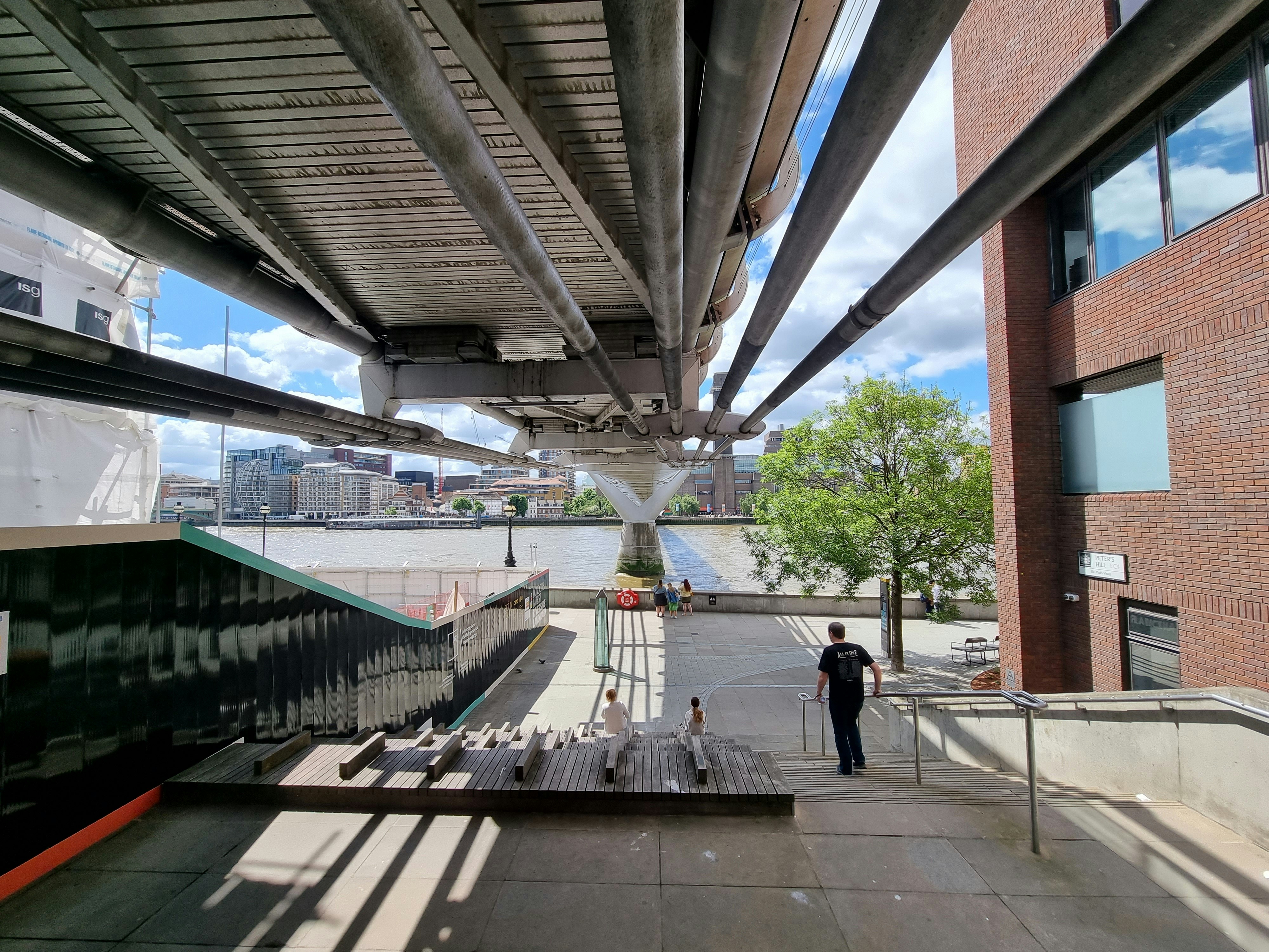 A man walking down a walkway under a bridge photo – Free Grey Image on ...