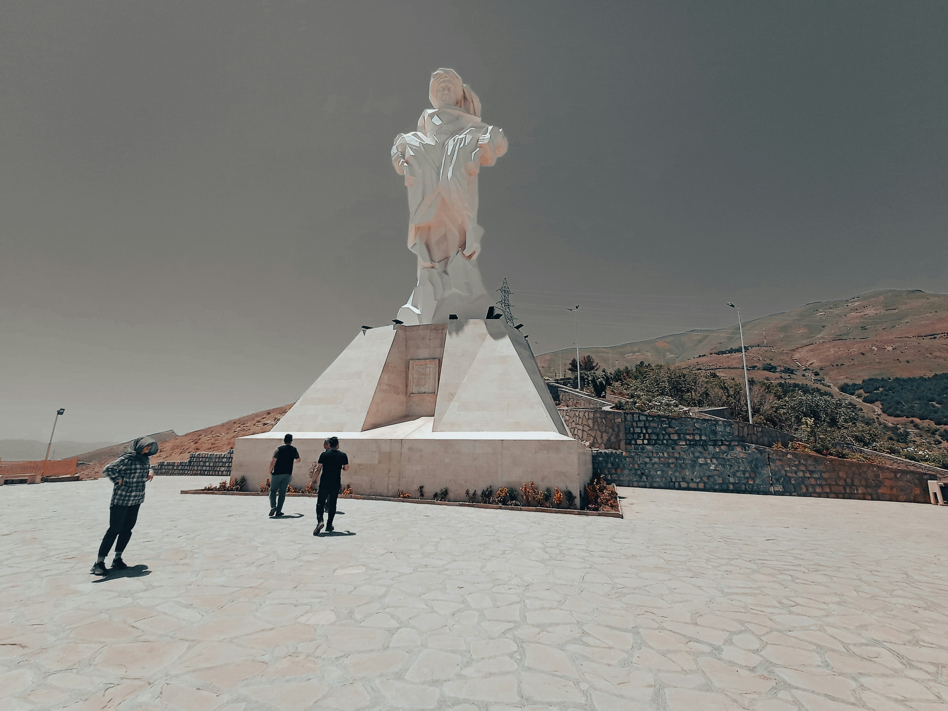 Large statue on a pedestal with people walking nearby under a clear sky.
