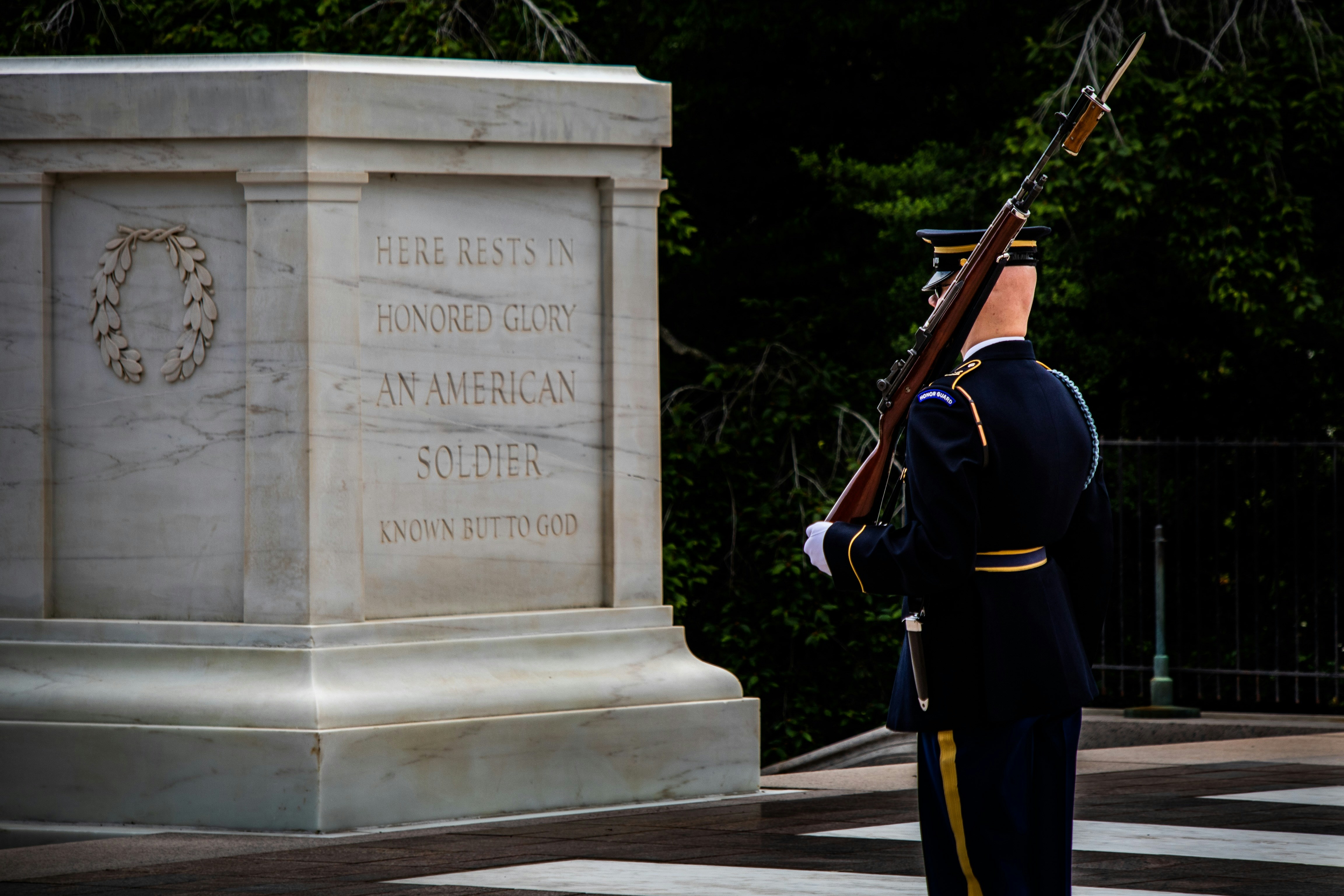 Sentry in uniform stands watch before a solemn monument.