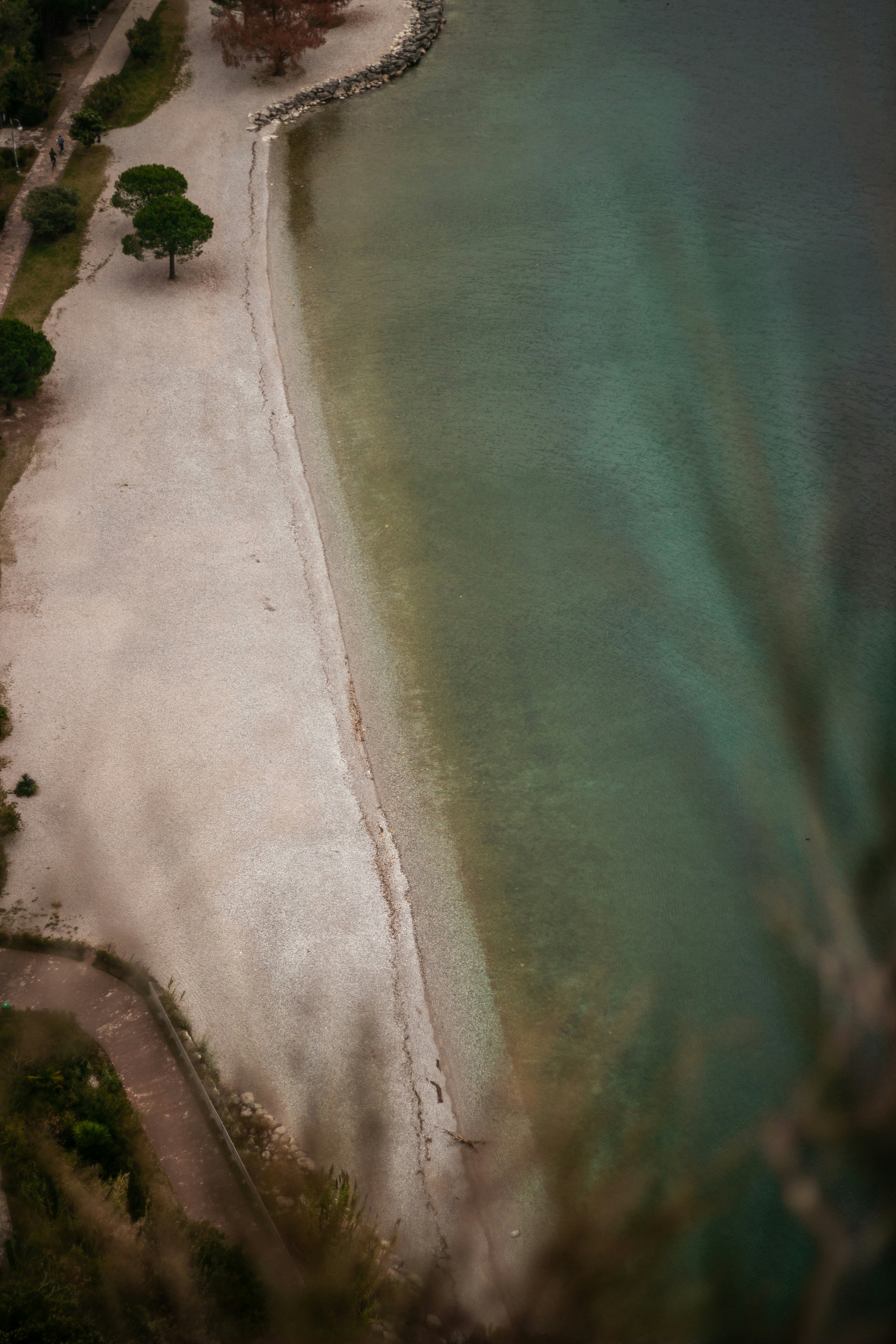A tranquil beach scene featuring a gentle curve of sand meeting the clear waters, framed by lush greenery. The composition highlights the peaceful coexistence of land and sea.