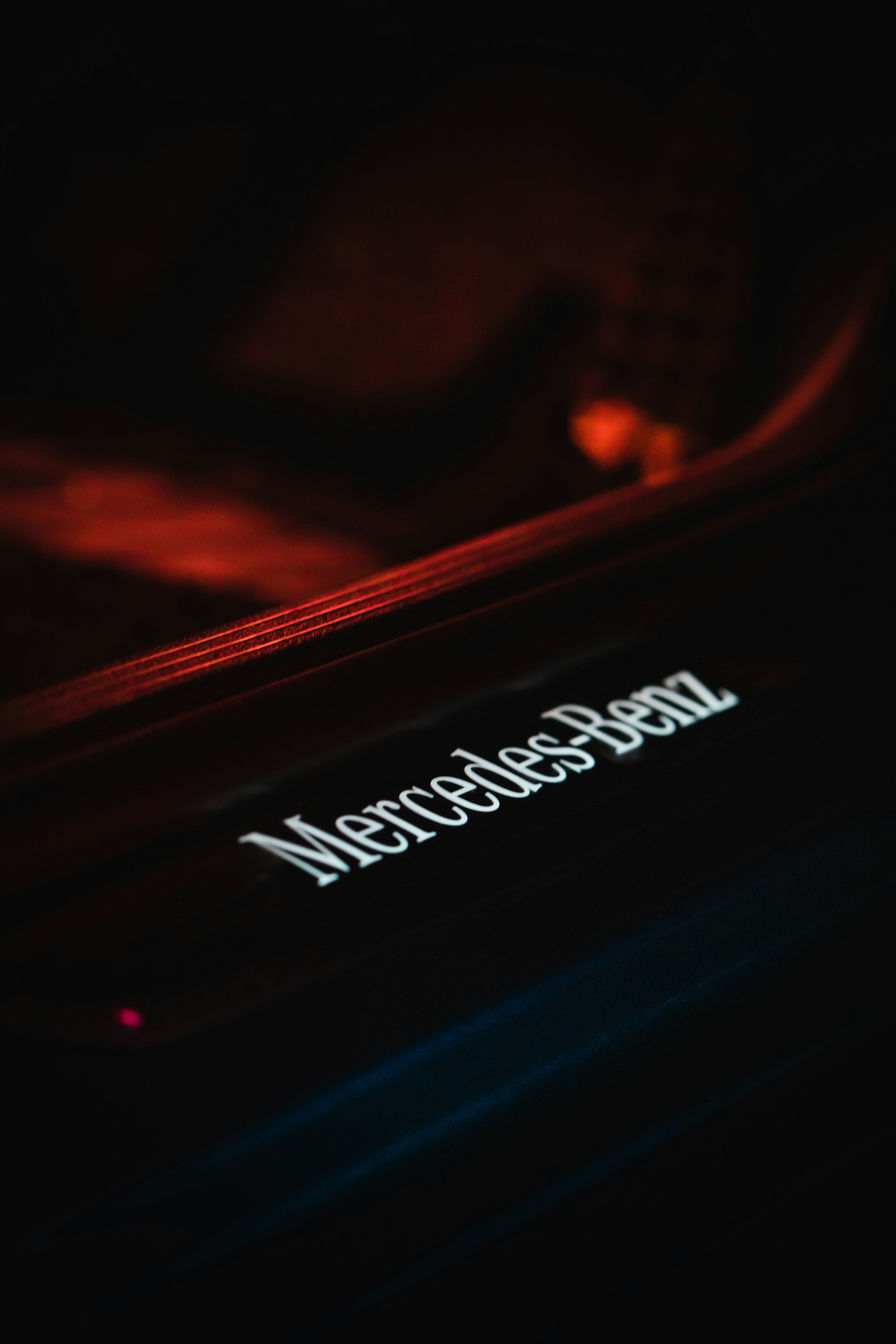 Close-up of a Mercedes-Benz logo on a glossy car panel, bathed in red ambient light.
