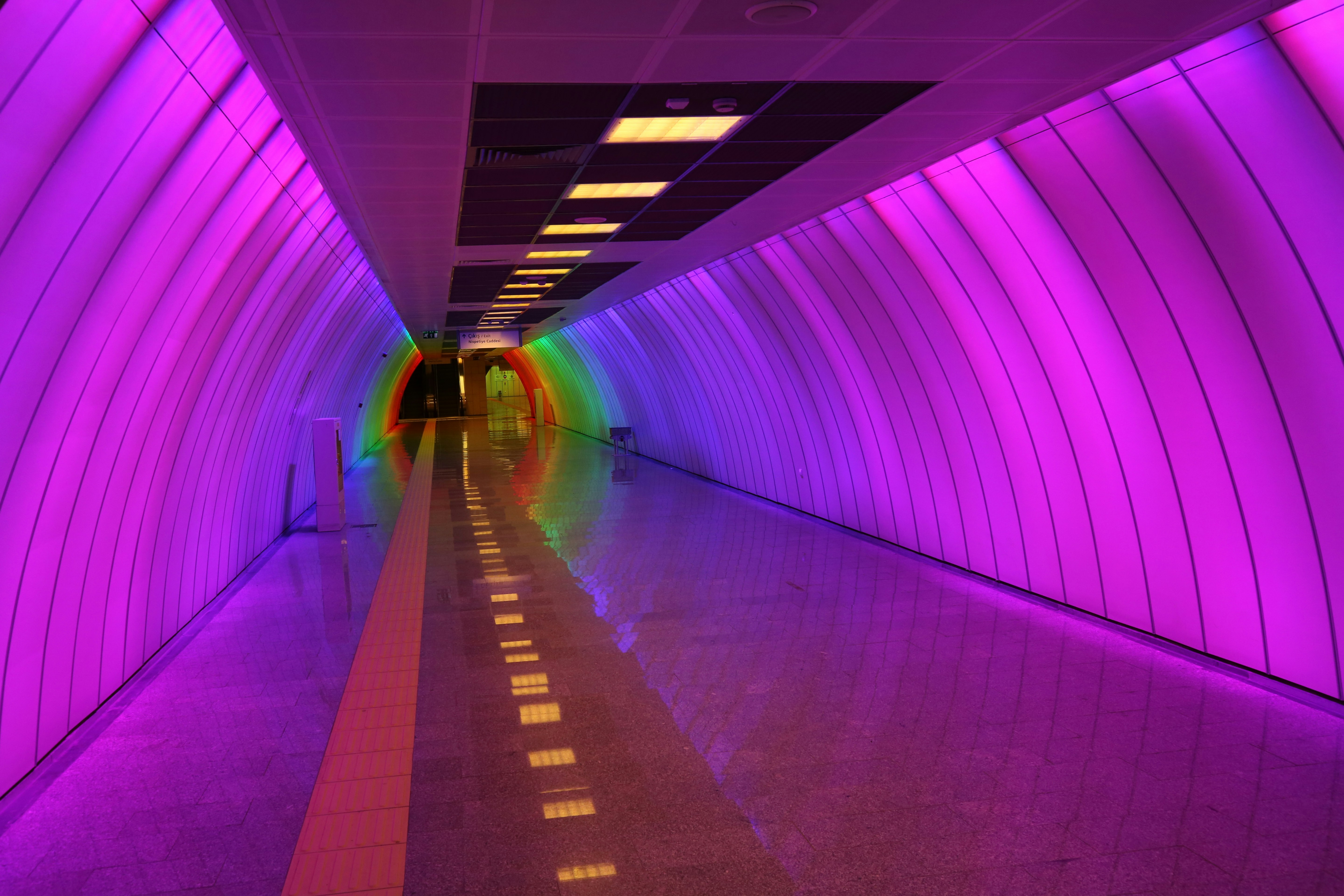 Vibrant illuminated tunnel featuring a spectrum of colors reflecting off polished surfaces, creating a surreal atmosphere.