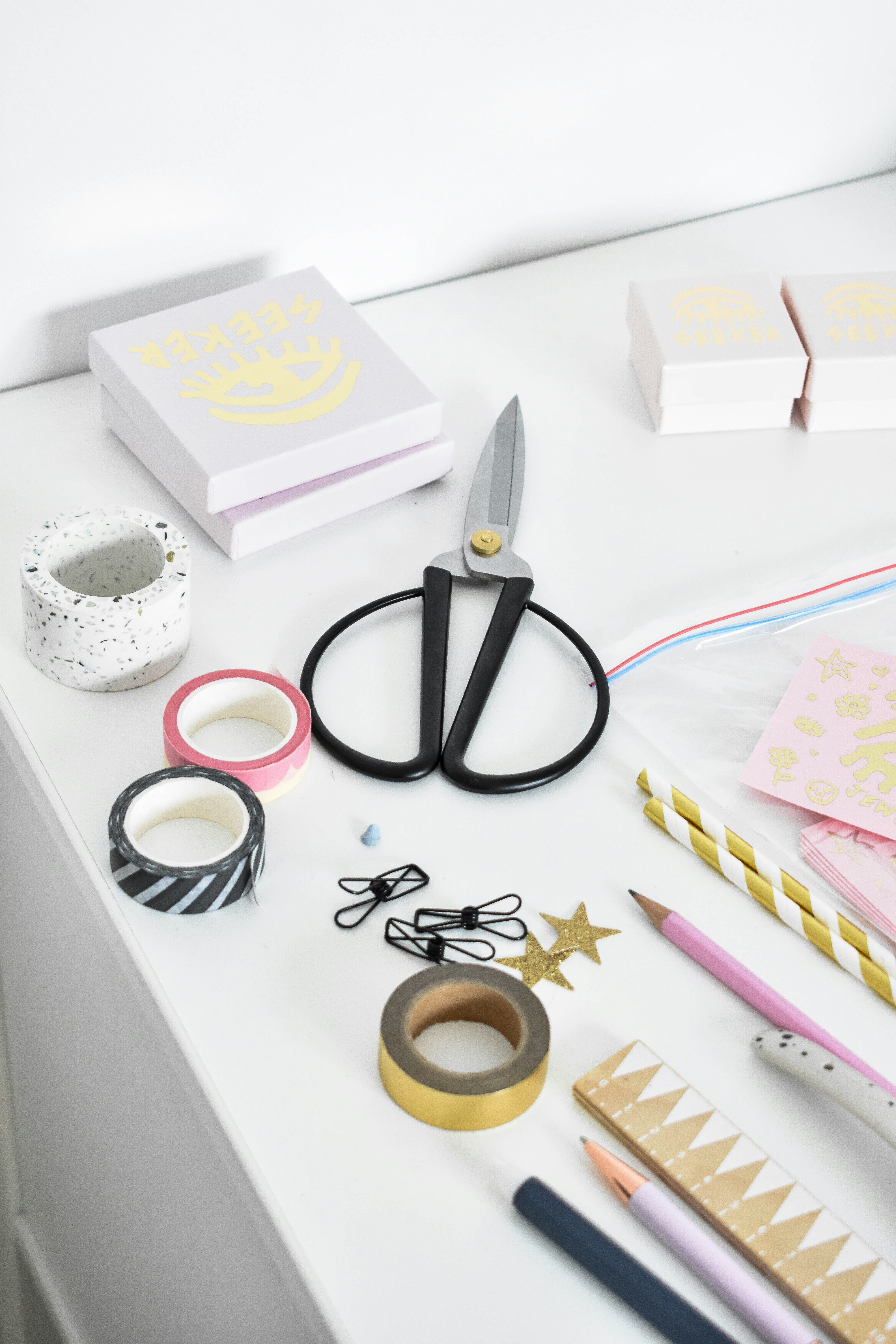 A collection of crafting tools and supplies, including scissors, washi tape, and decorative papers, arranged on a clean surface.