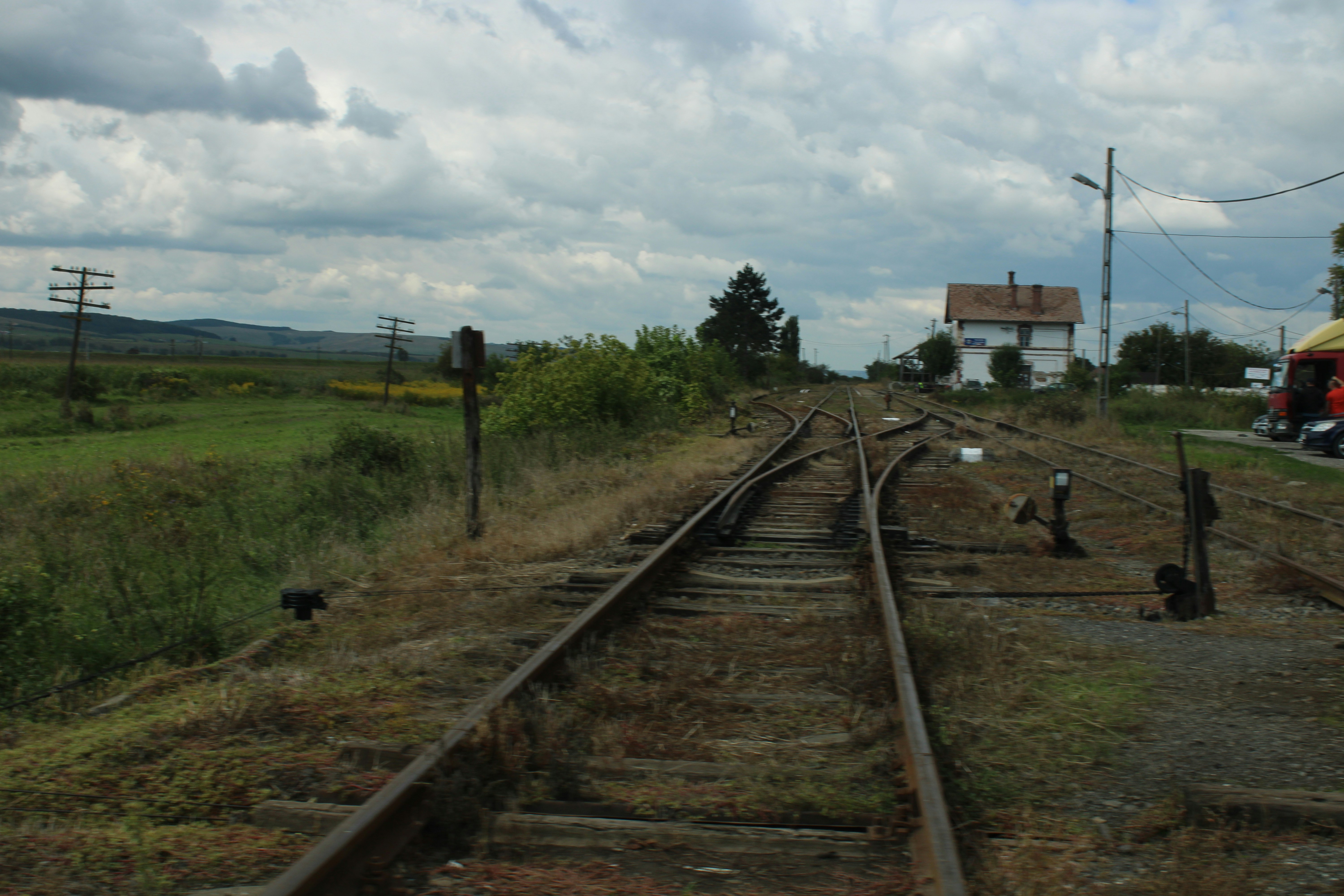 Abandoned railway tracks diverging in a rural landscape, framed by overcast skies and distant hills.