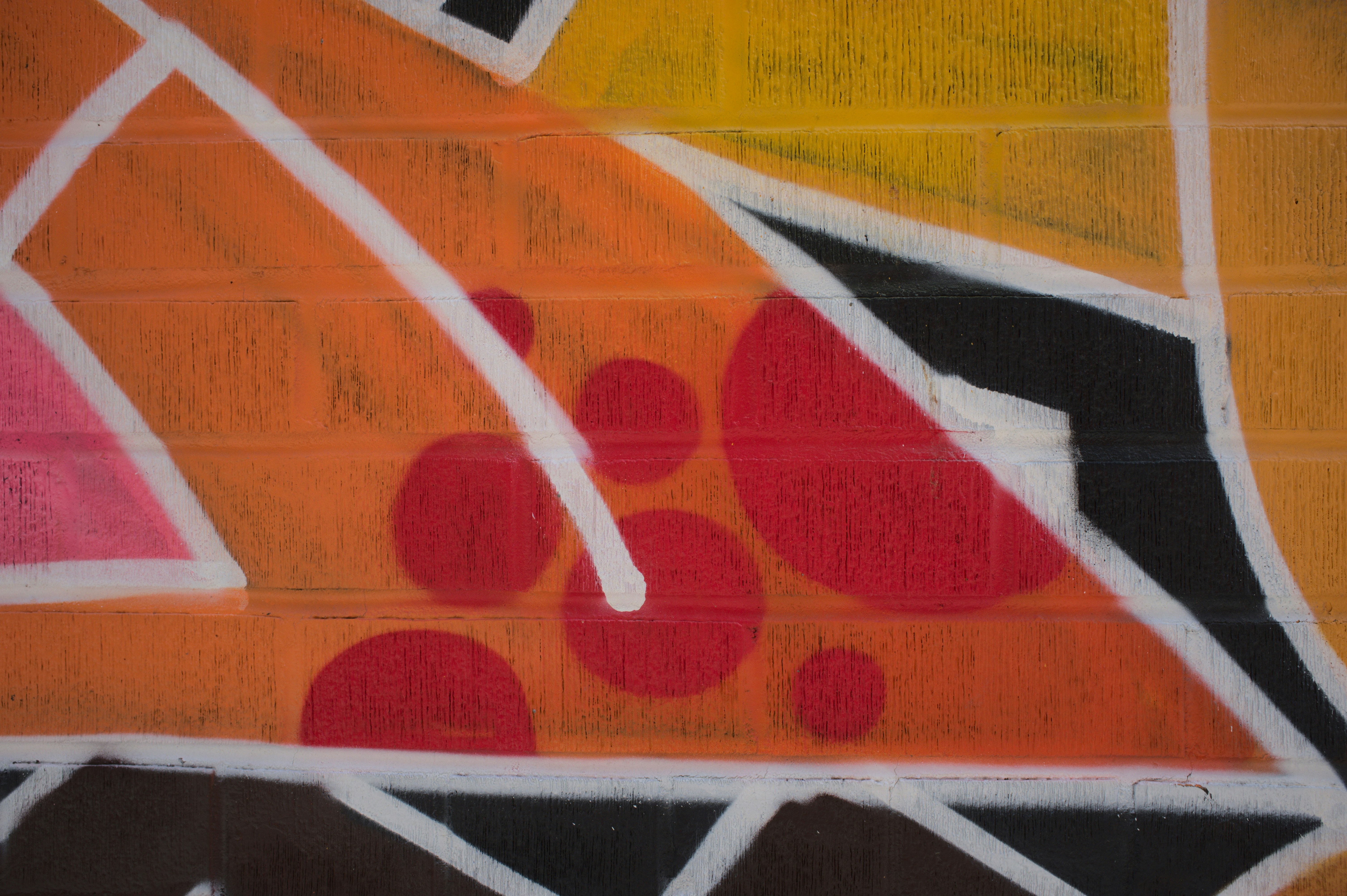 Abstract Graffiti Pattern on Orange Brick Wall With Red Circles - A close-up shot of a brick wall covered in abstract graffiti. The main color is orange, with red circles, white lines, and black and pink shapes. The graffiti appears to be a modern and stylized design, showcasing an urban art form.