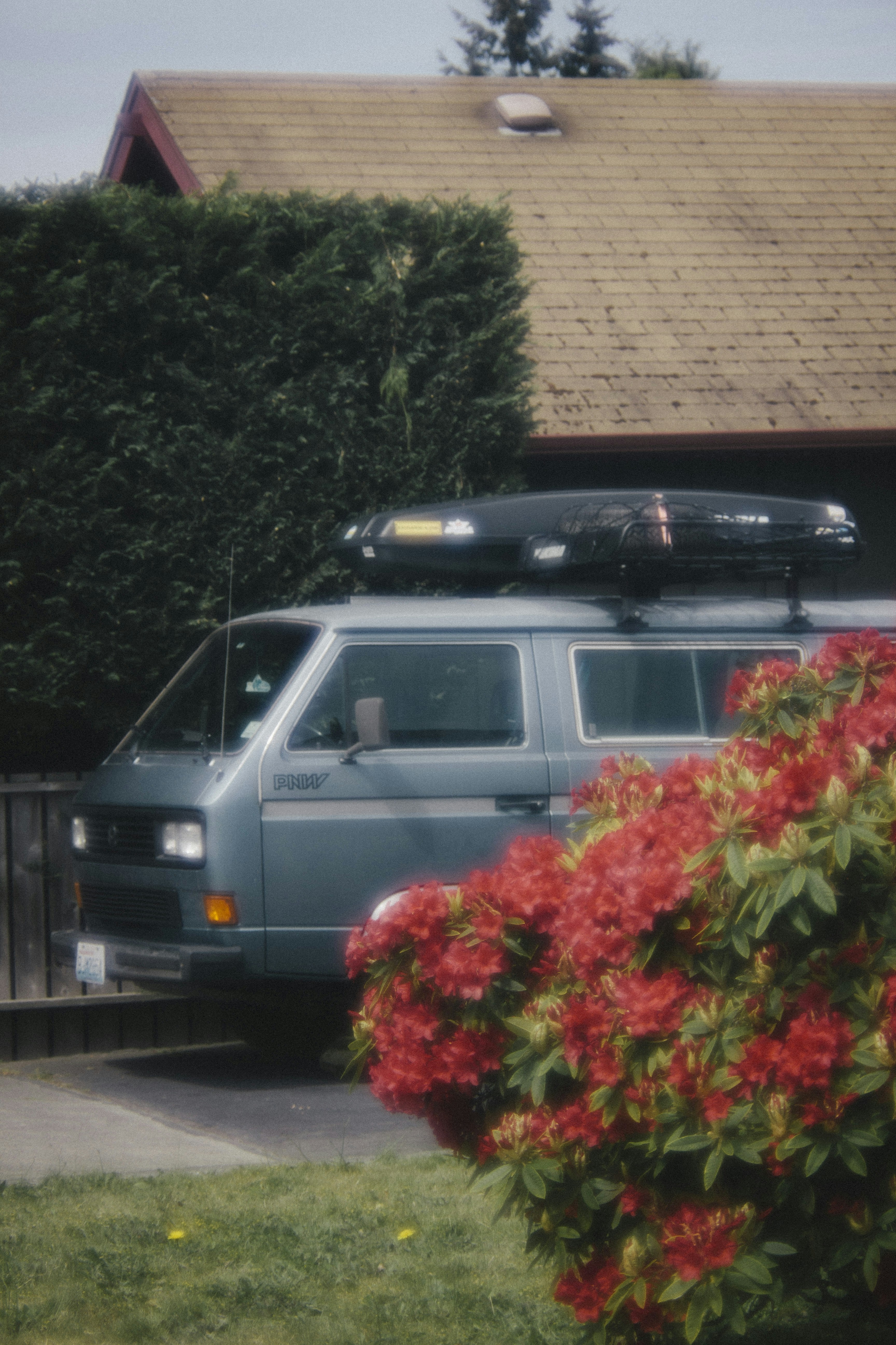 Blue van at the hedge-choked driveway with a roof cargo box