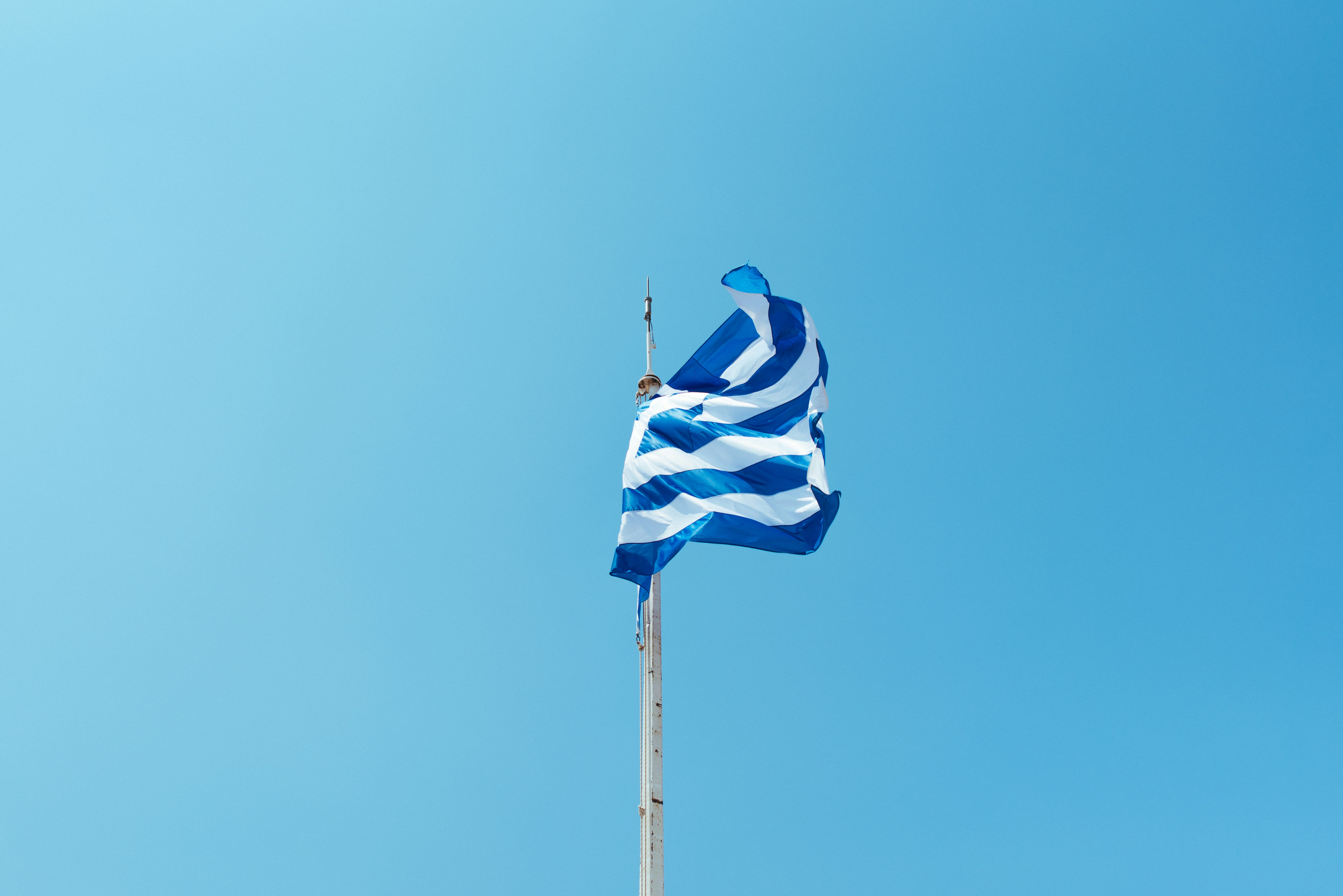 Greek Flag Unfurls at the Crest Against a Pristine Cerulean Sky