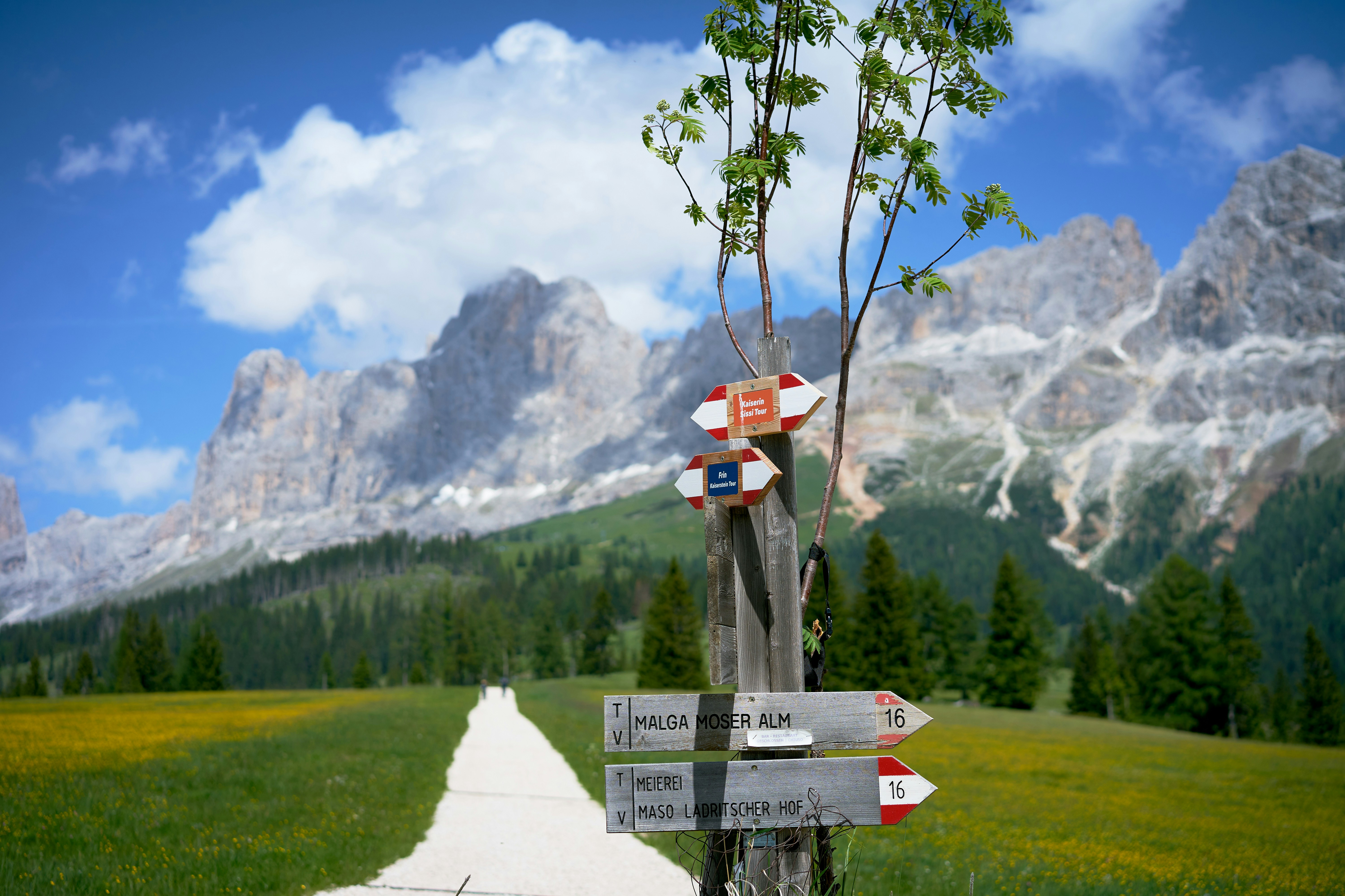 Trail signpost stands against a backdrop of towering mountains and a clear blue sky.