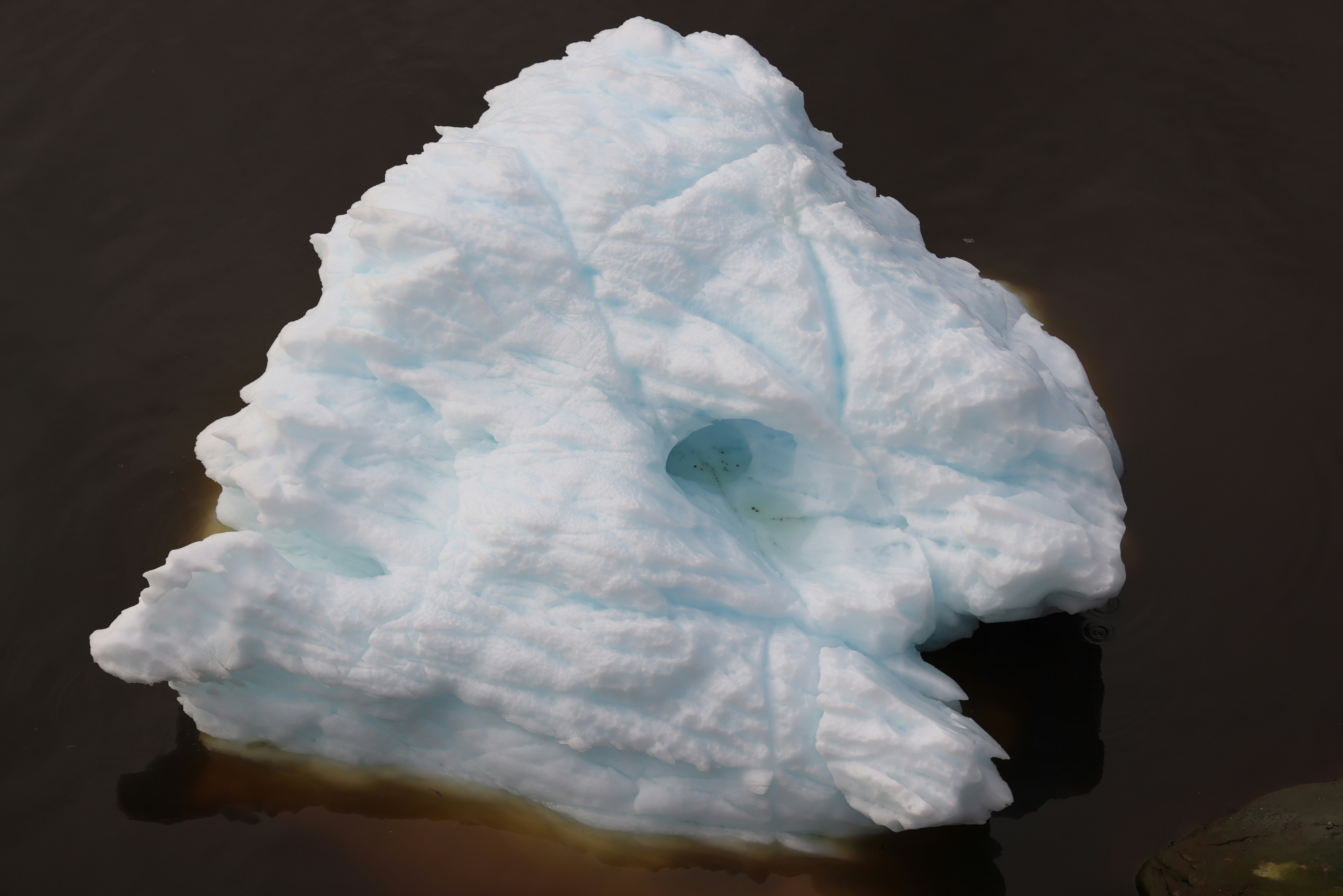 A solitary ice chunk floating in dark waters, showcasing intricate textures and a hint of blue hue. The scene highlights the delicate balance of nature's elements.