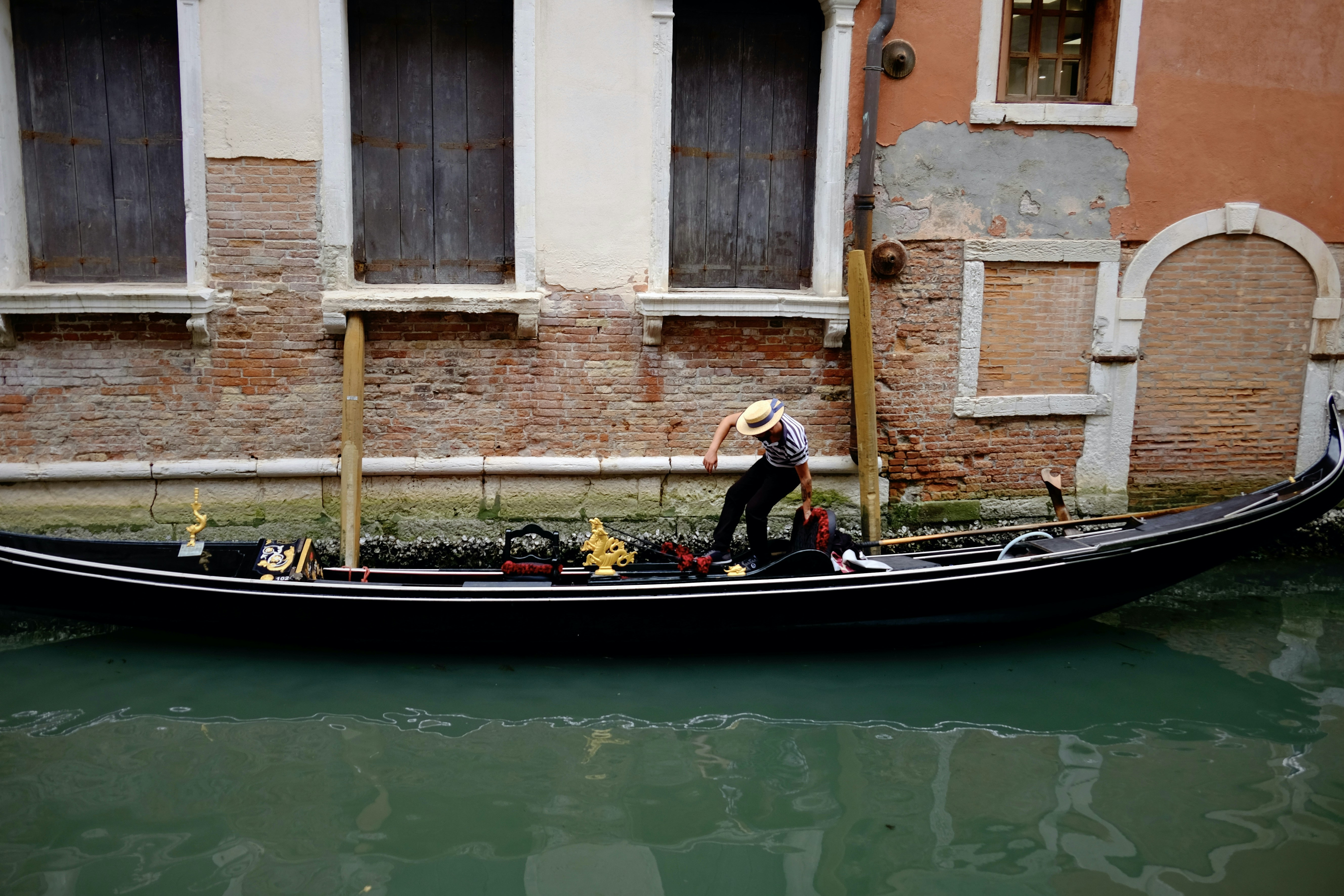 Straw-Hatted Gondolier at a Venetian Canal Against Weathered Brick