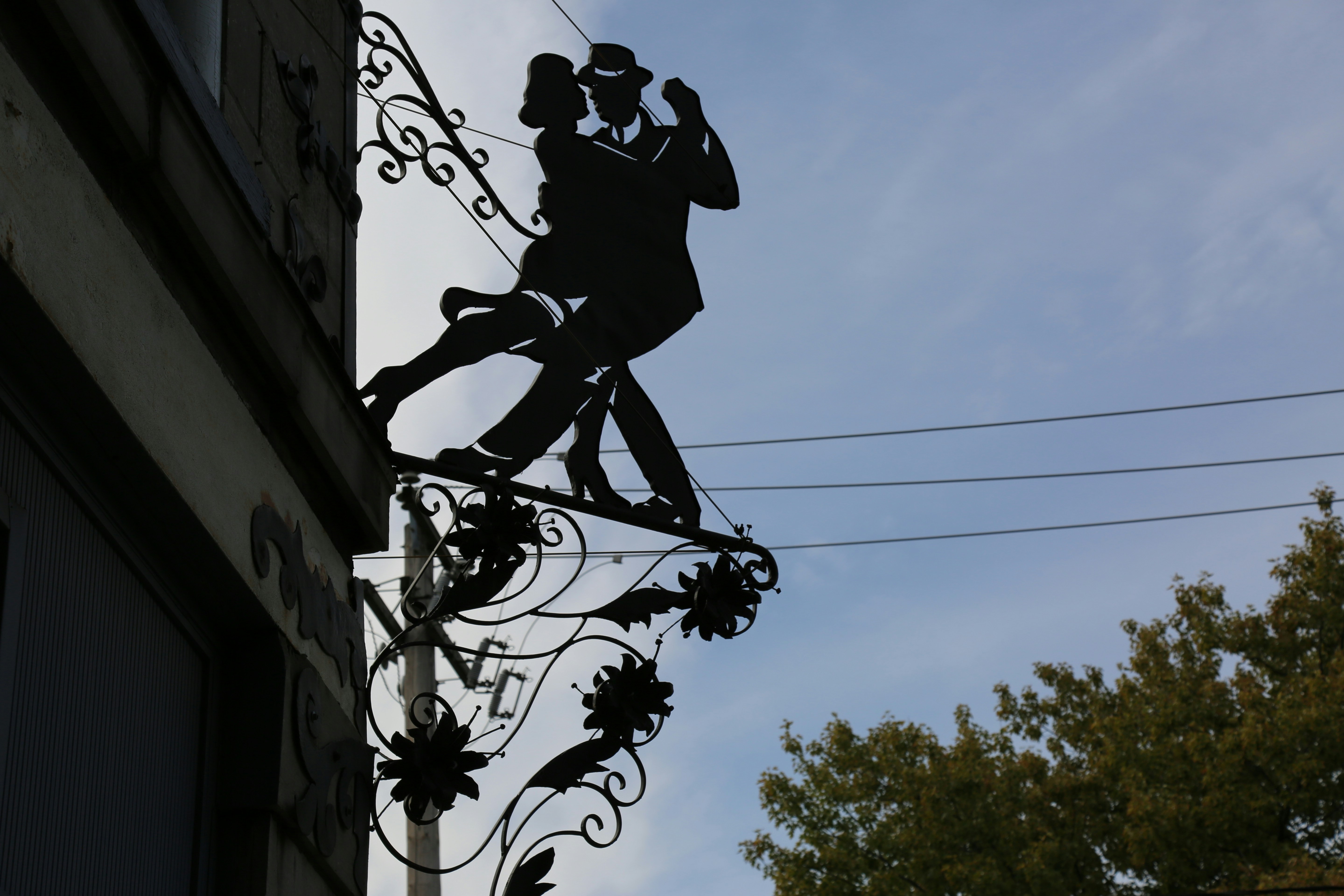 Silhouette Waltz on a Wrought-Iron Sign Against a Clear Sky