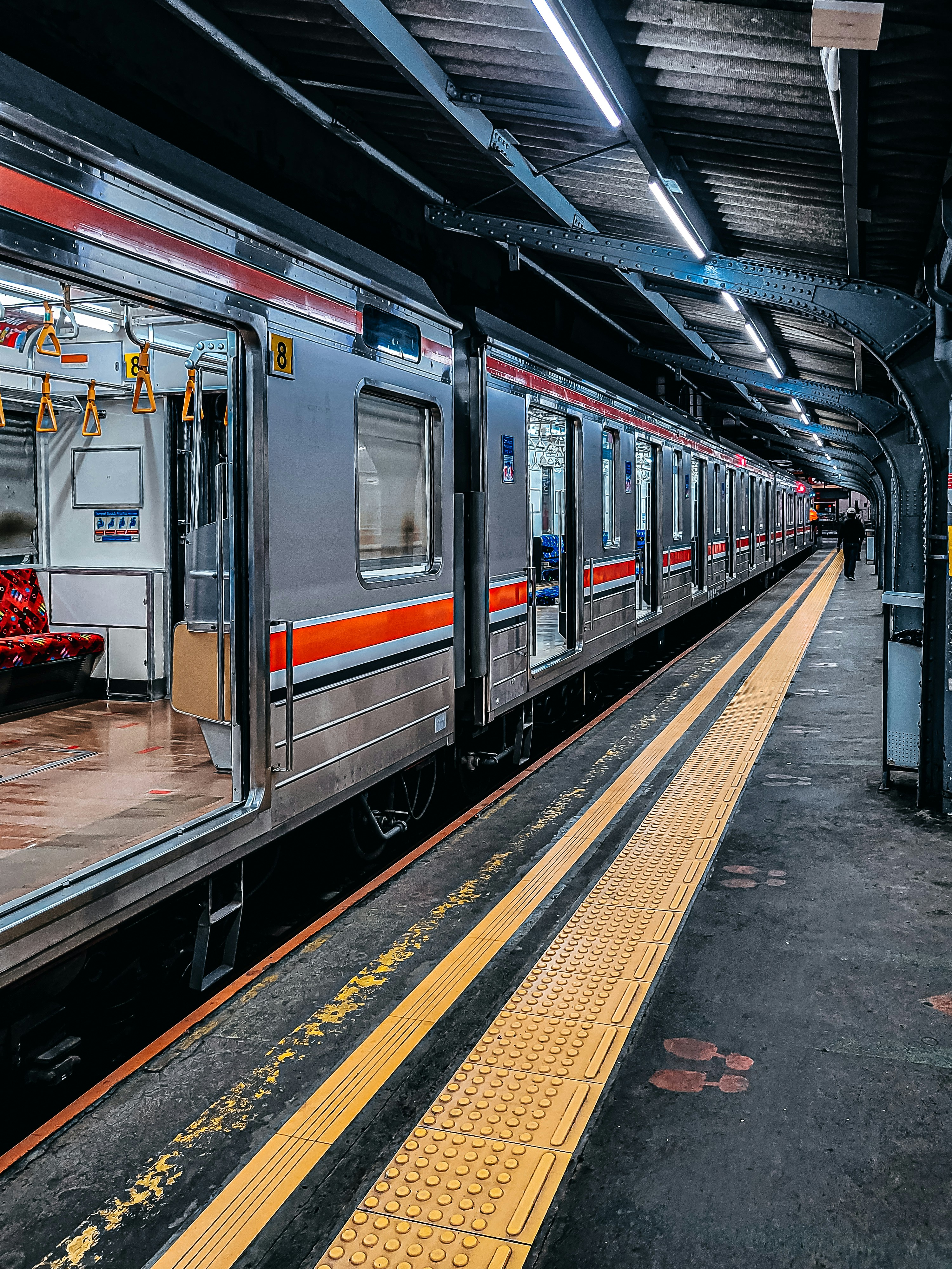 Interior view of a subway station with open train doors revealing empty seats and a clean platform. Yellow safety lines guide passengers along the platform.