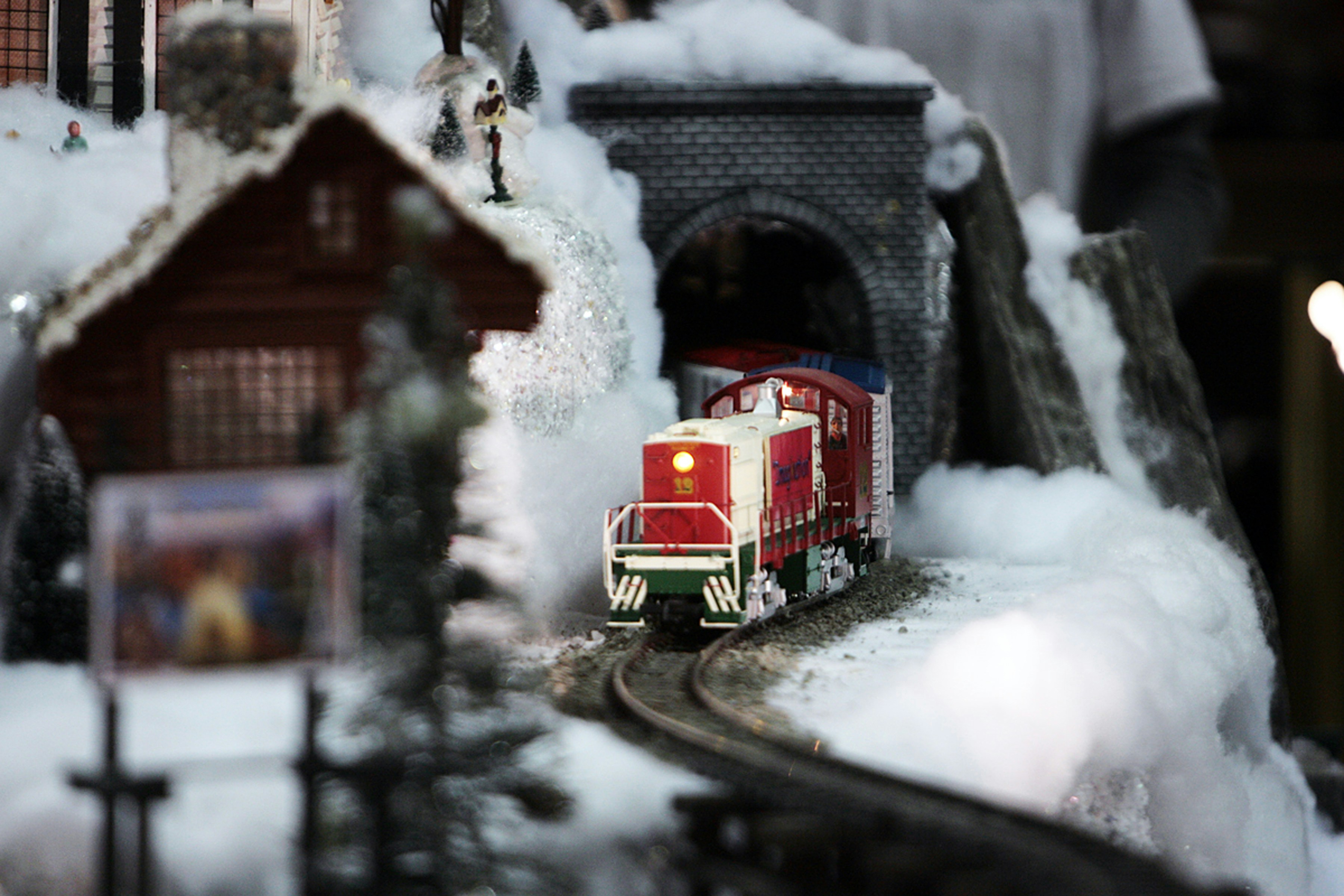Snow-dusted miniature train diorama features a bright red locomotive winding along a curved track through a wintry village.