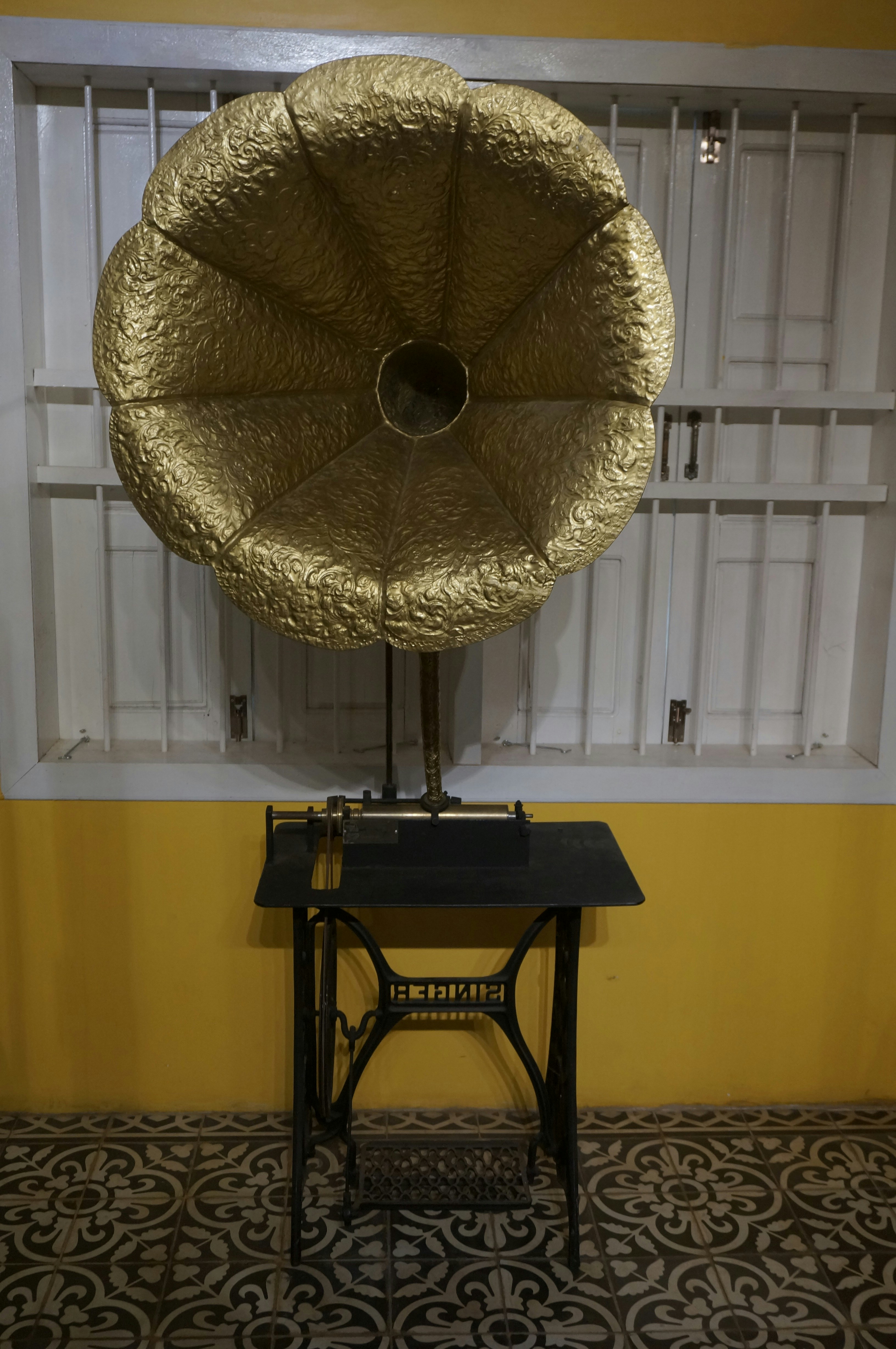 Vintage gramophone with a large, ornate golden horn displayed against a yellow wall, capturing the essence of musical nostalgia.